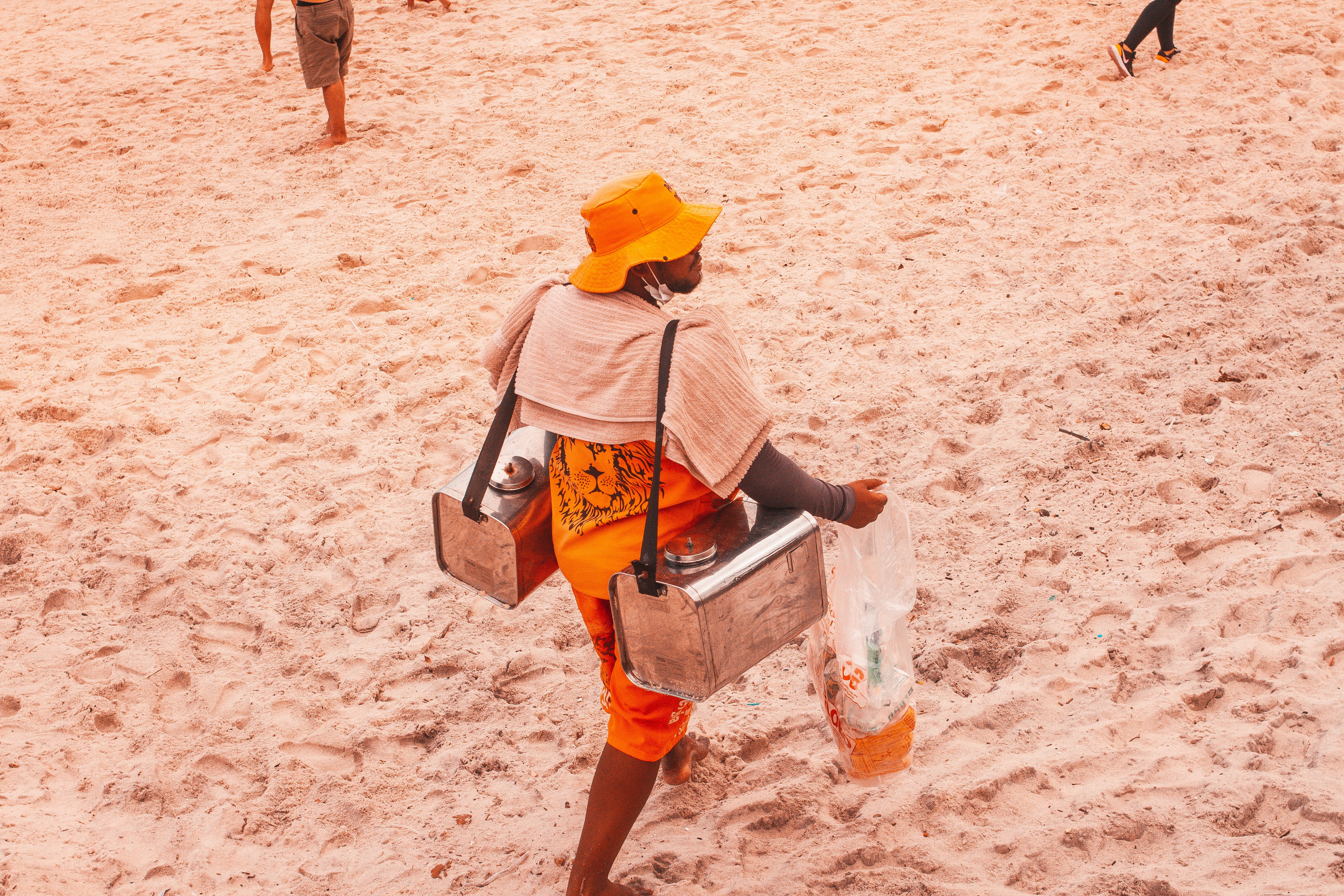 Sunlit Beach Carry: A Vendor with Buckets Traverses the Dune-Soft Sand