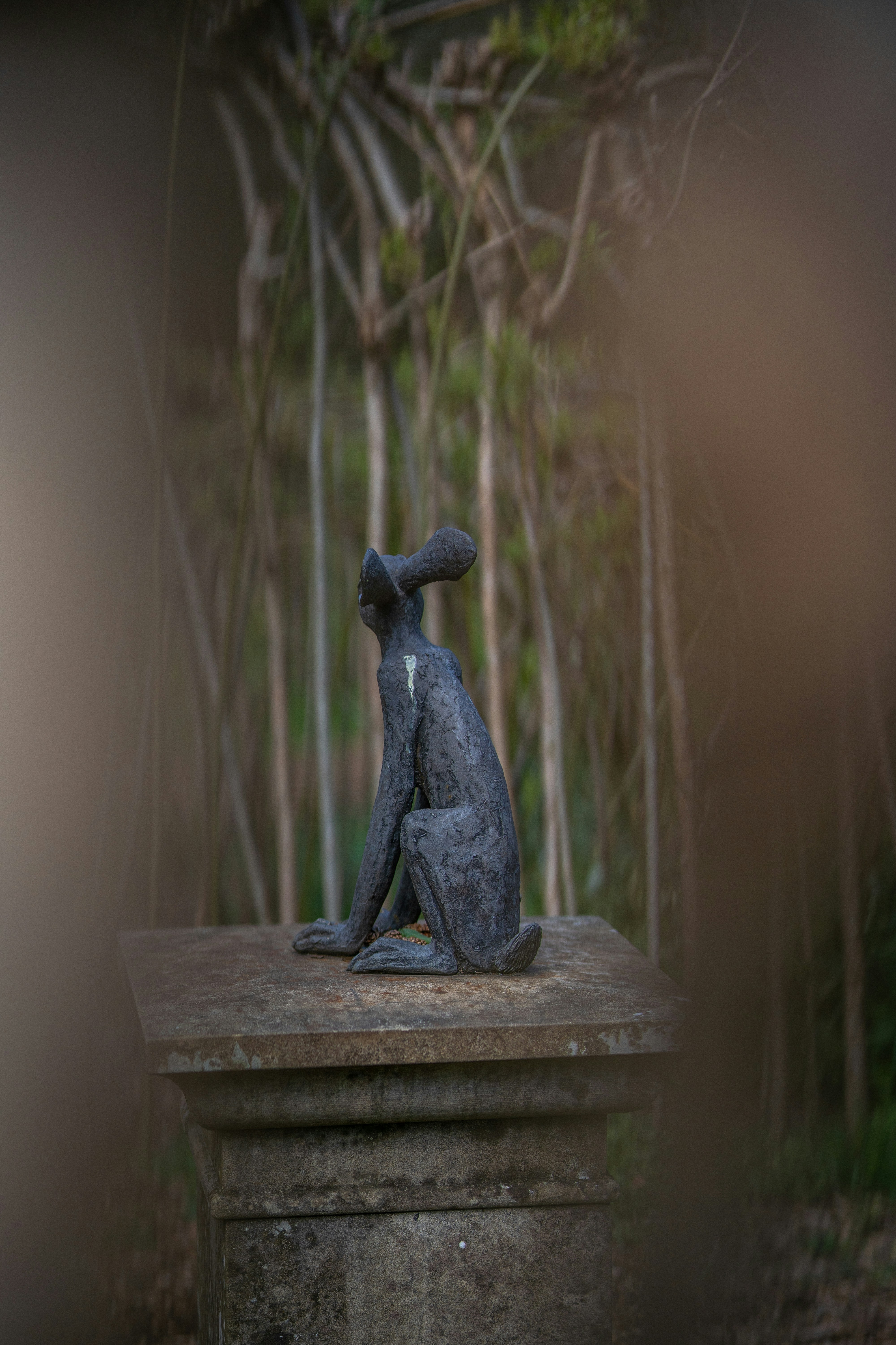 Stoic Figurine on a Weathered Pedestal, Framed by Quiet Foliage
