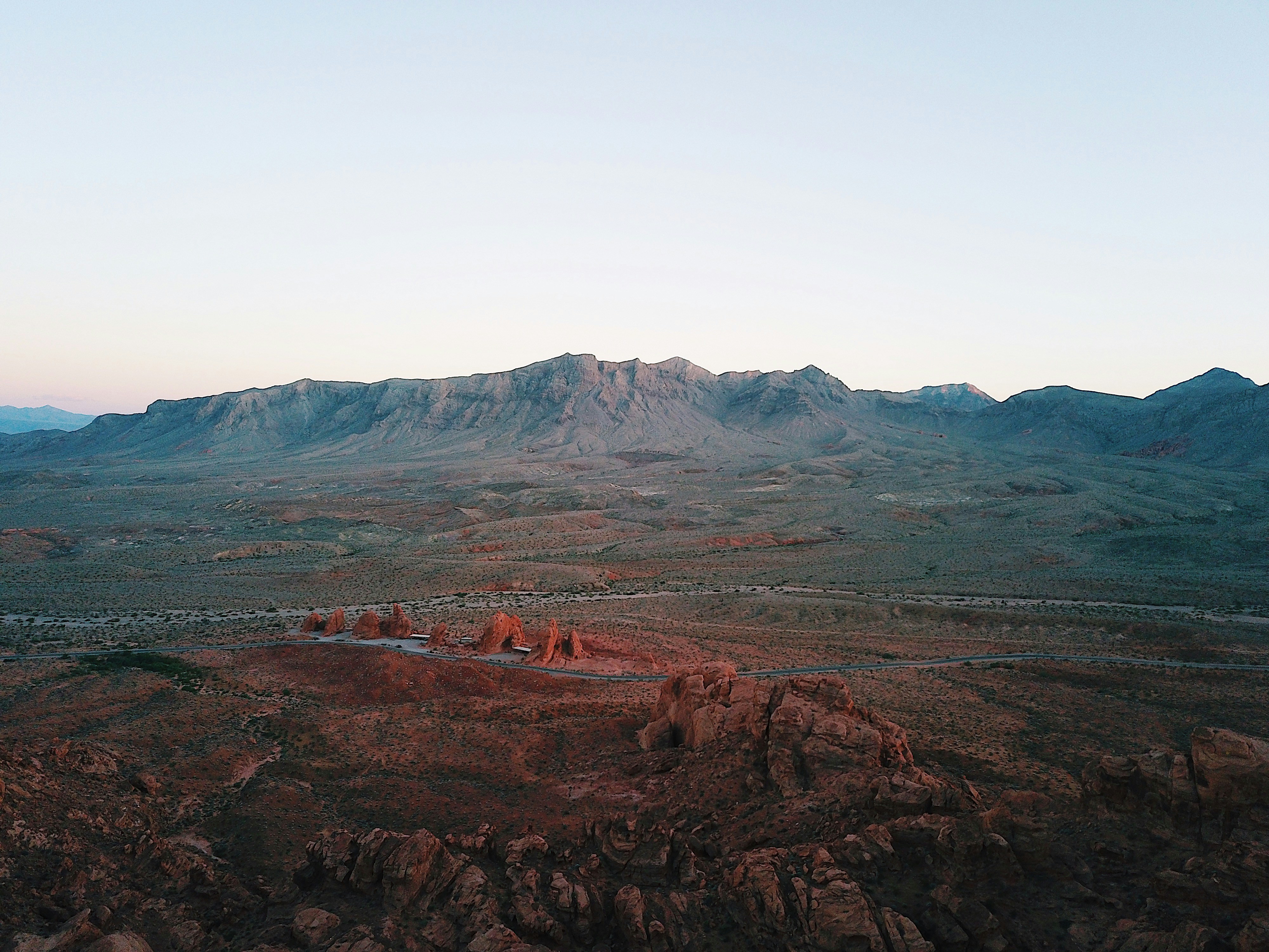 Expansive view of Nevada's Valley of Fire with rugged red rock formations and distant mountains under a fading sunset sky.
