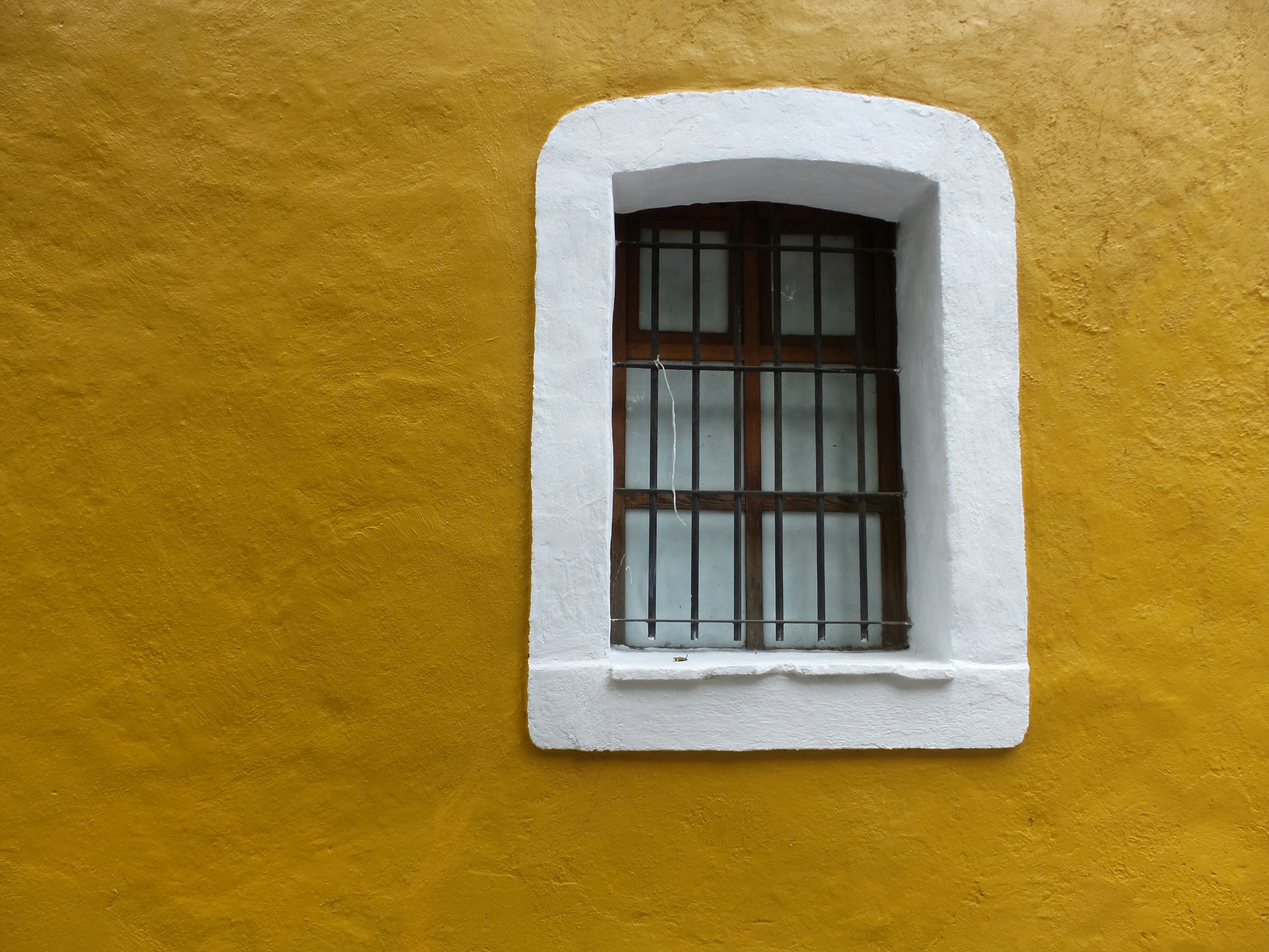 A wooden window framed in white, set against a vibrant yellow wall, showcasing a blend of texture and color.