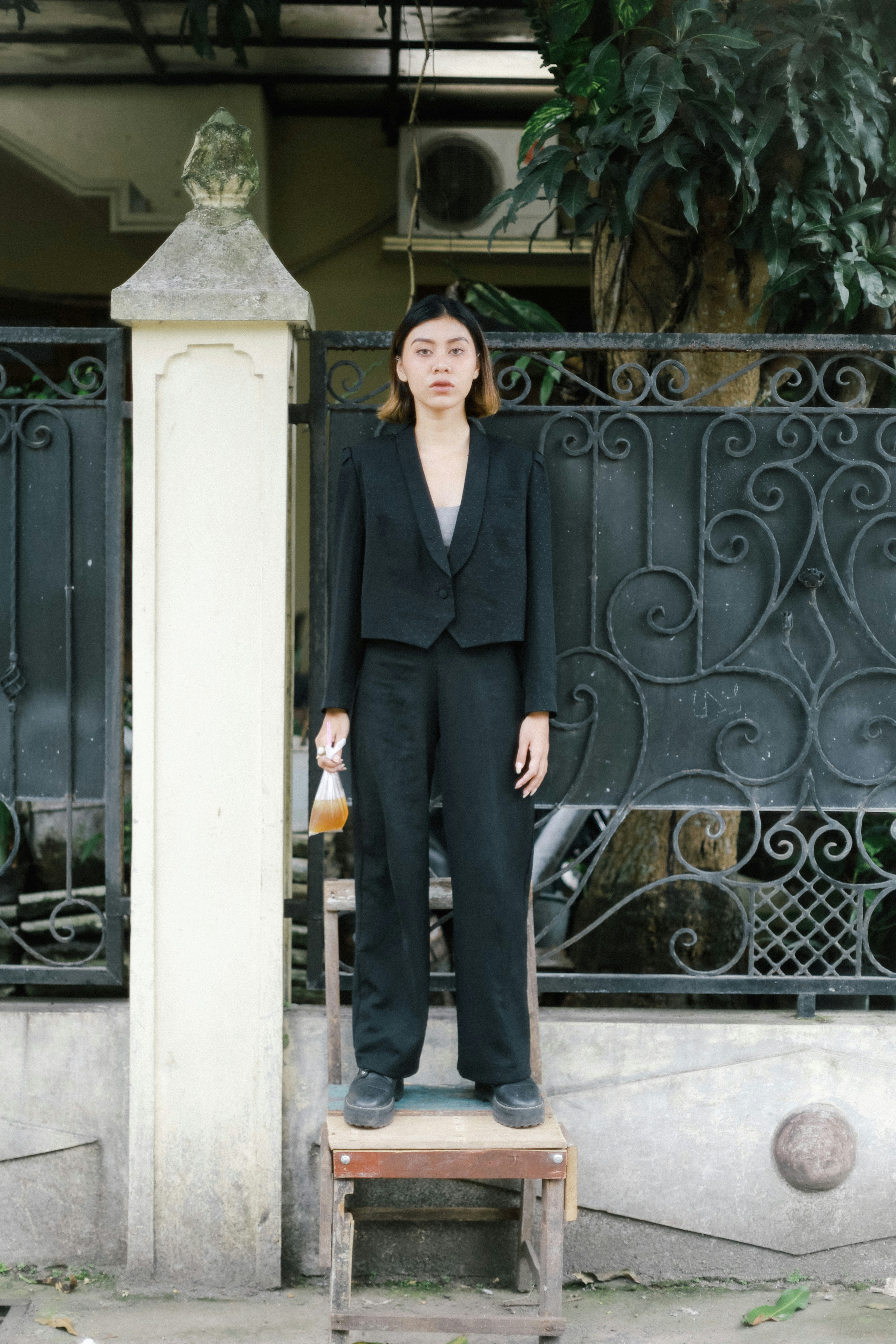 Noir Suit on a Small Stage: A poised figure before an ornate iron gate.
