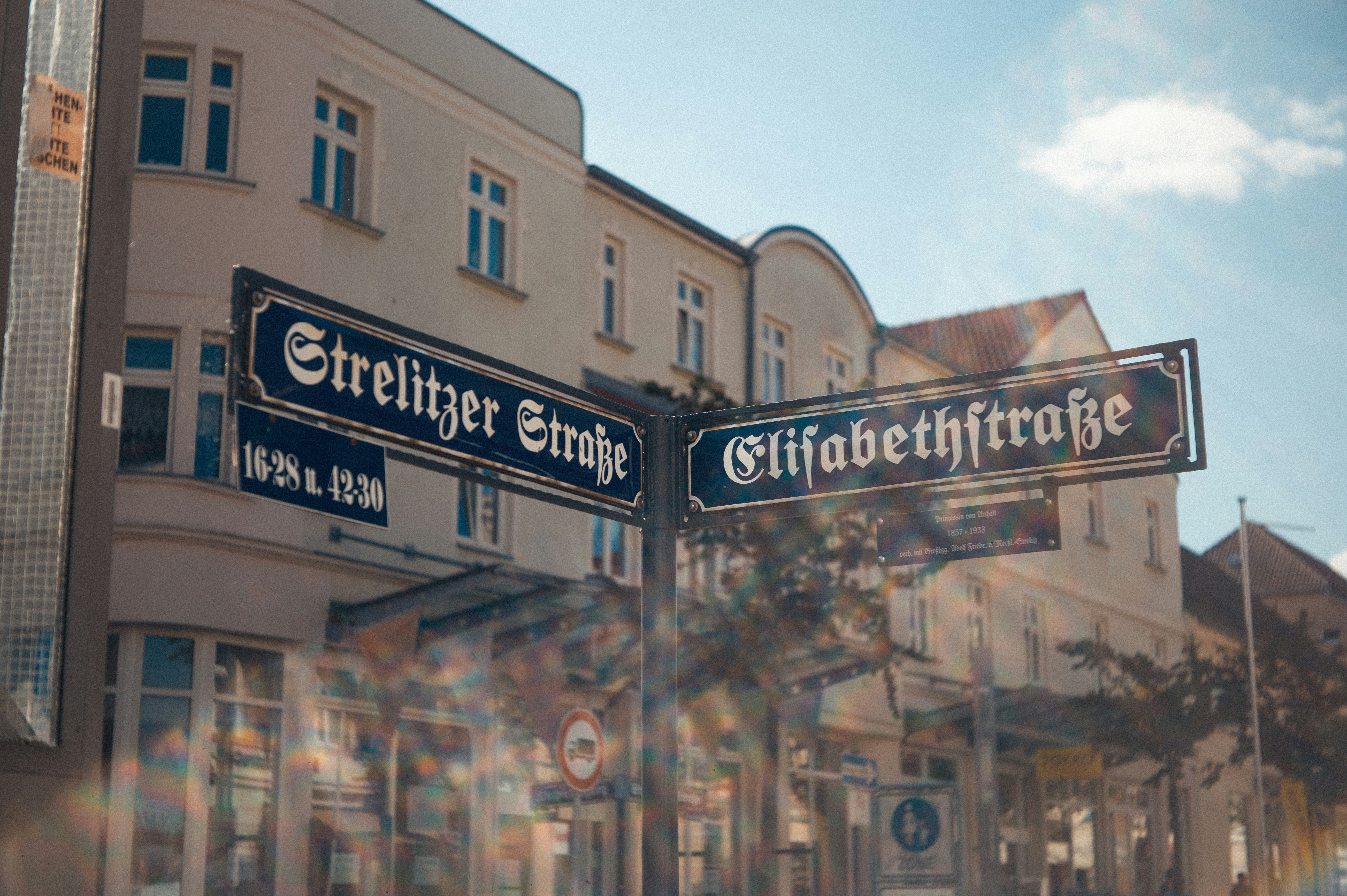 Street signs in front of classic German architecture under a clear blue sky.