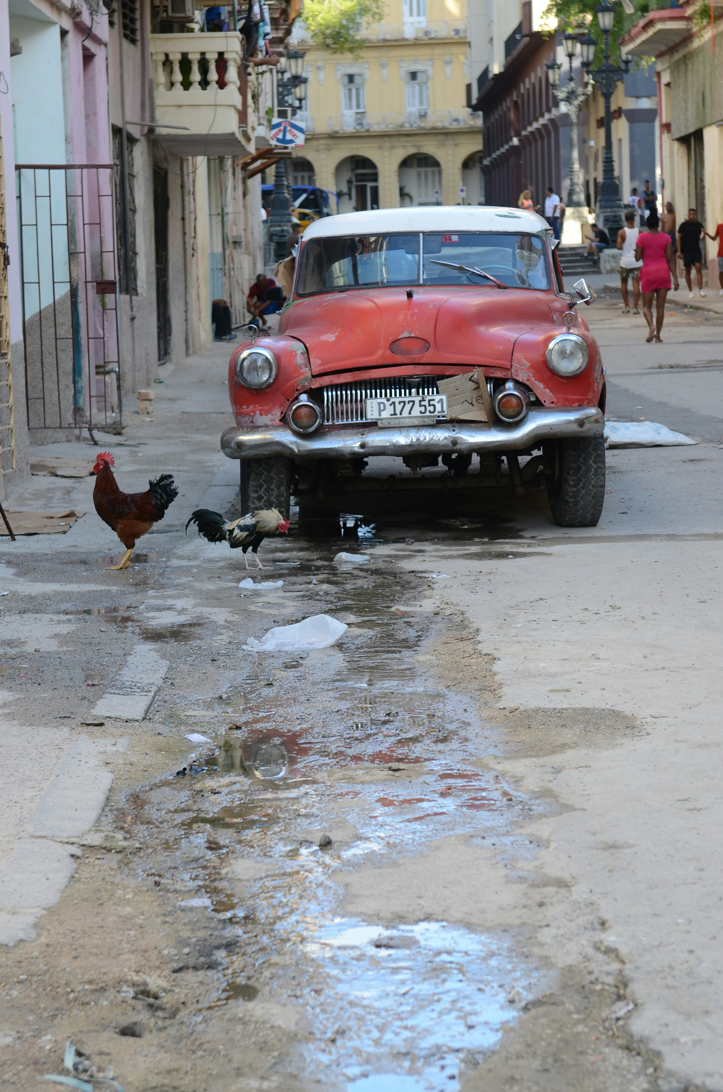 Rust and Reflection: A 1950s Red Sedan Anchors a Sunlit Cuban Street