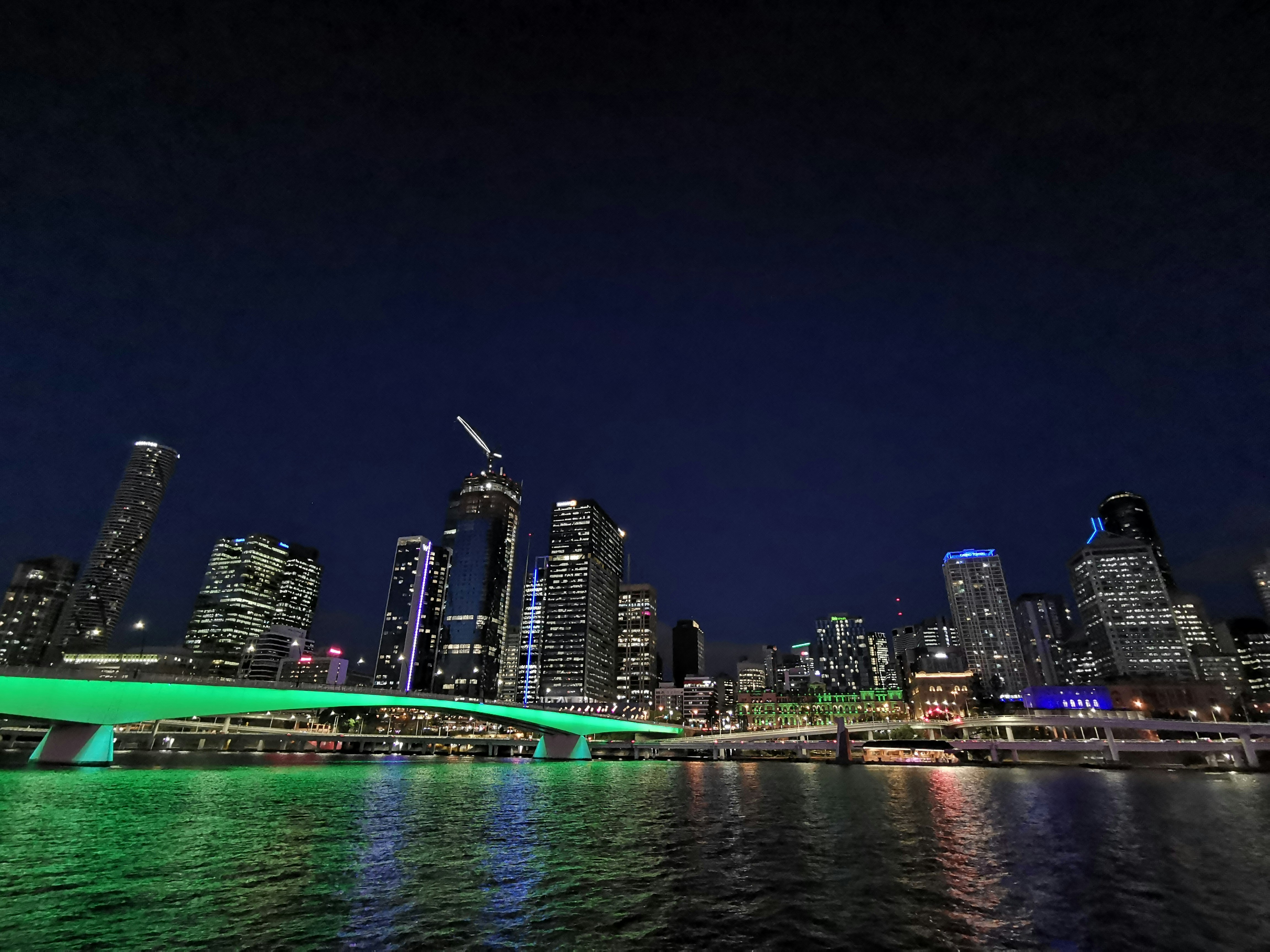 City skyline illuminated at night with vibrant green and blue lights reflecting on the water.