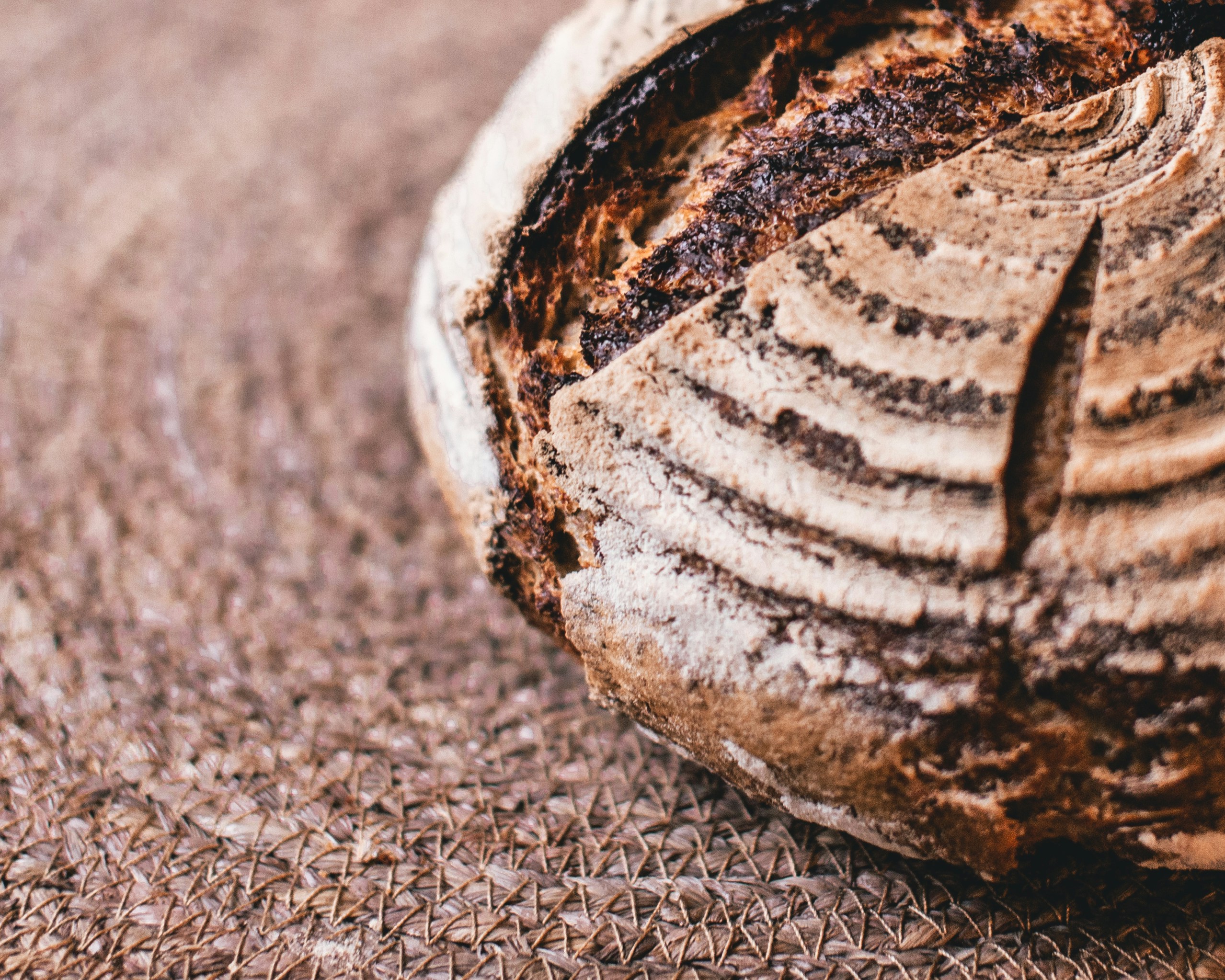 Close-up of a crusty loaf resting on a textured woven surface, highlighting rustic bread textures and flour-dusted ridges.