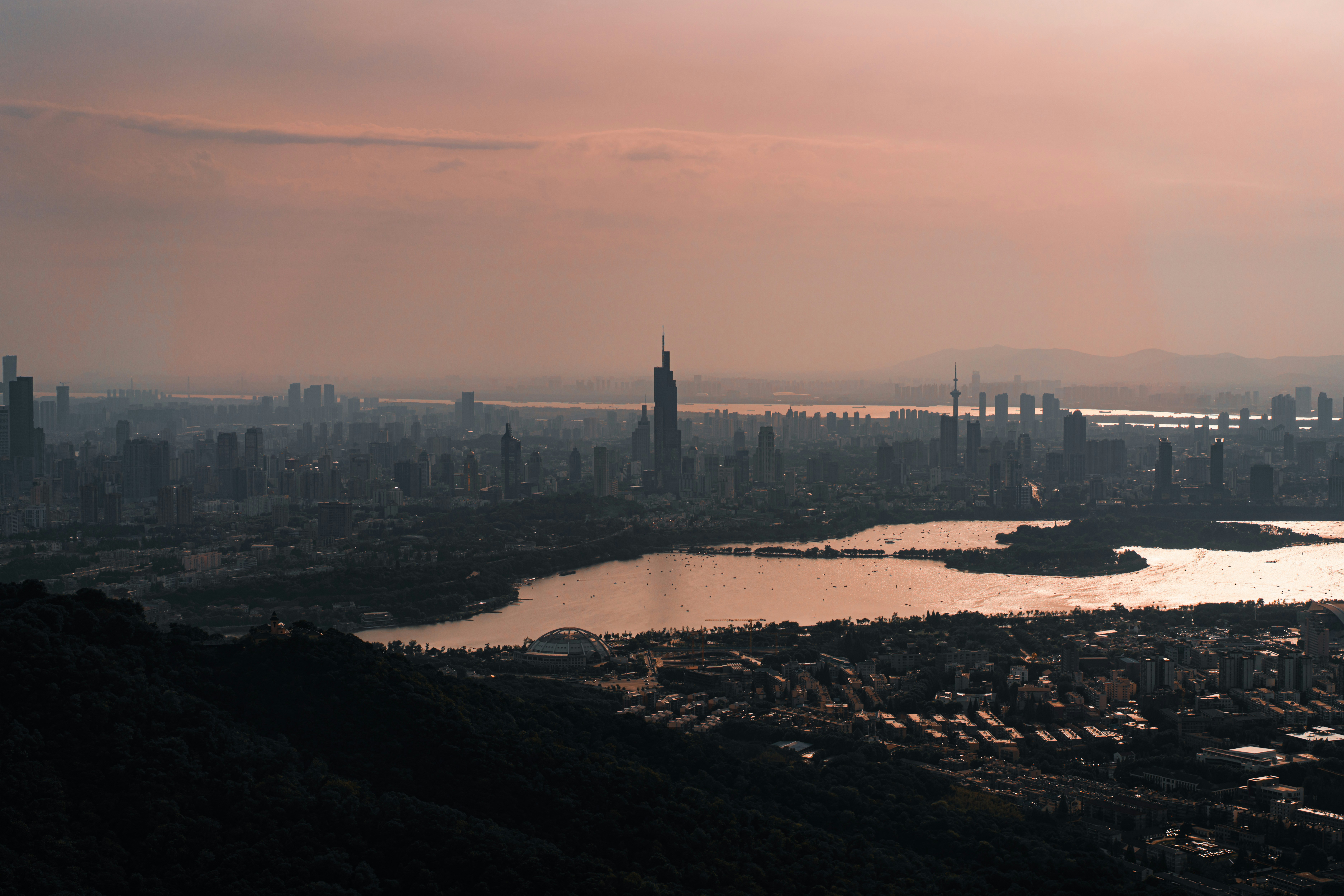 A panoramic view of a sprawling city skyline during twilight, with a prominent tower reflecting the warm hues of the setting sun over a winding river.