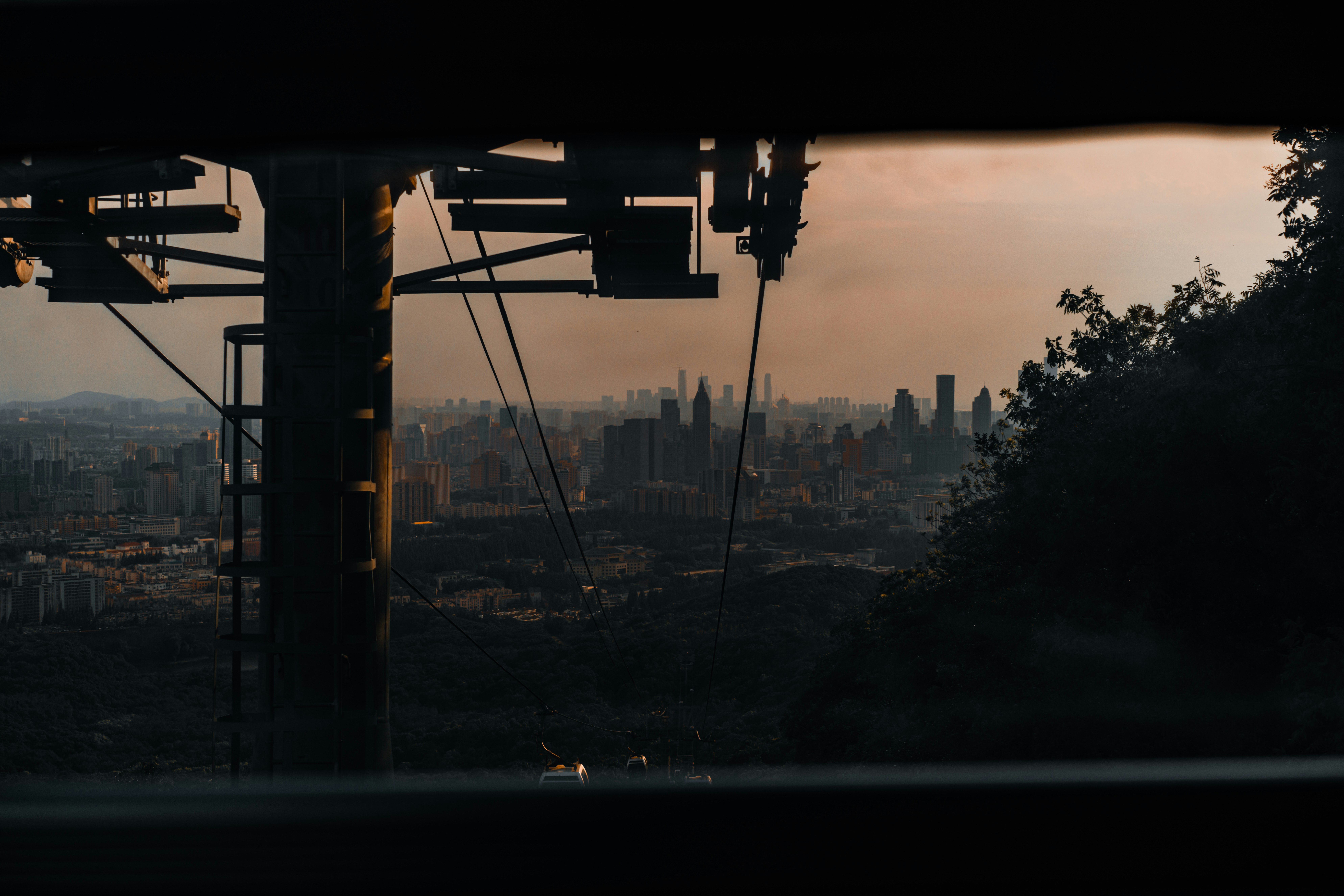 Cityscape of Nanjing viewed through the silhouette of a cable car structure at sunset.