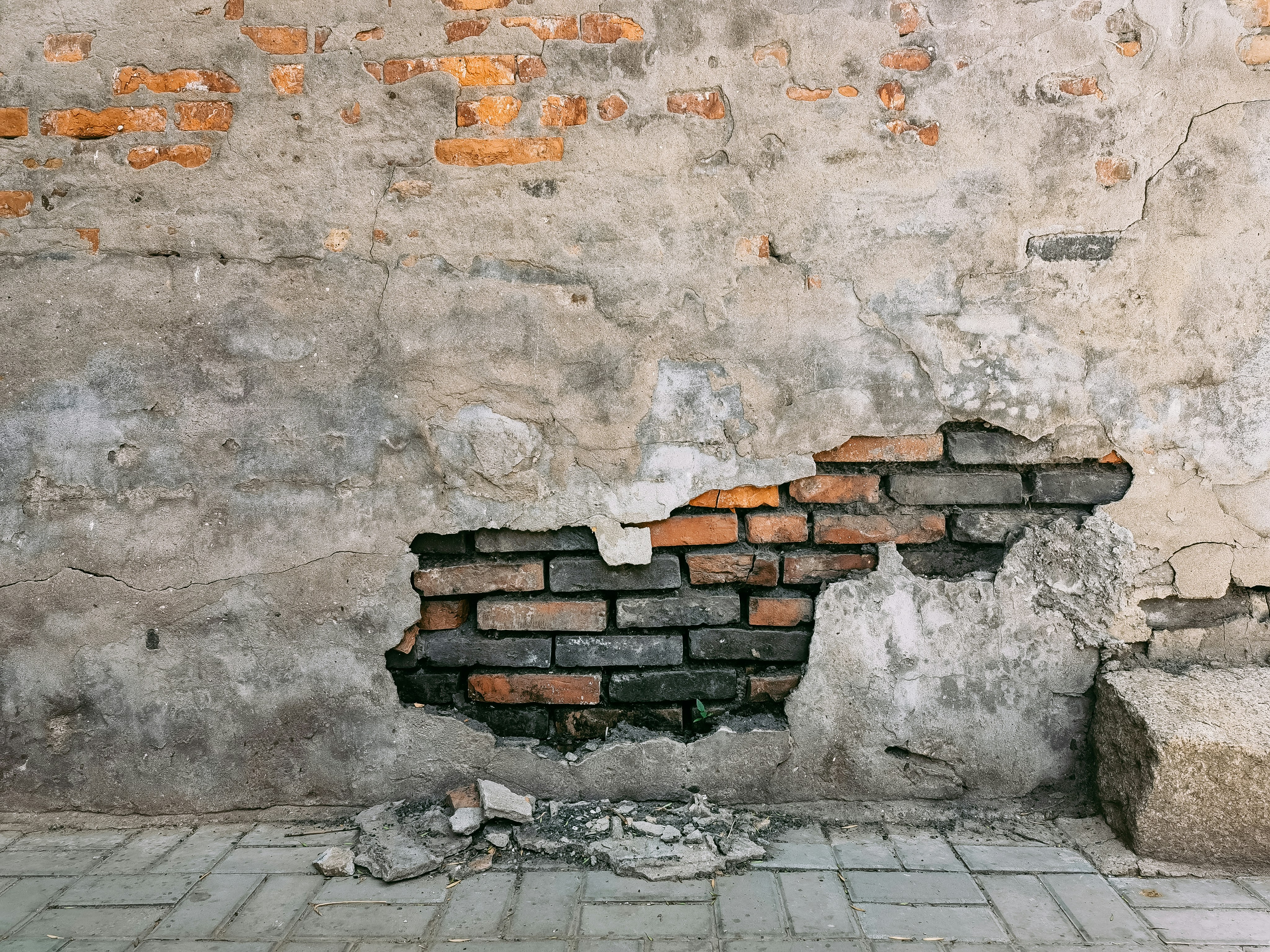 Cracked wall revealing exposed bricks and debris, illustrating the passage of time and wear on urban structures.