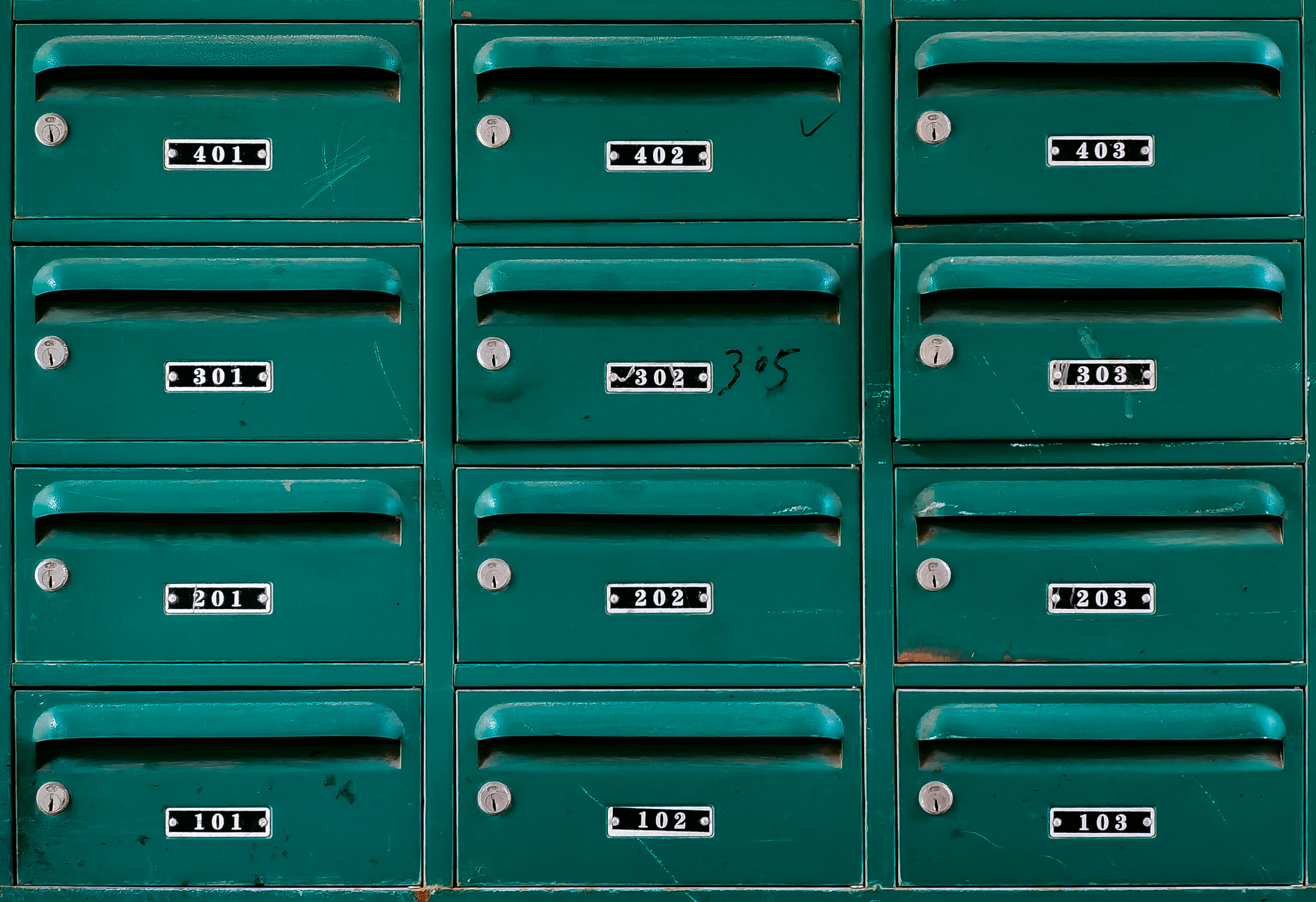 Row of vintage mailboxes showcasing a rich teal color, each adorned with black labels and handles, inviting curiosity about the stories they hold.
