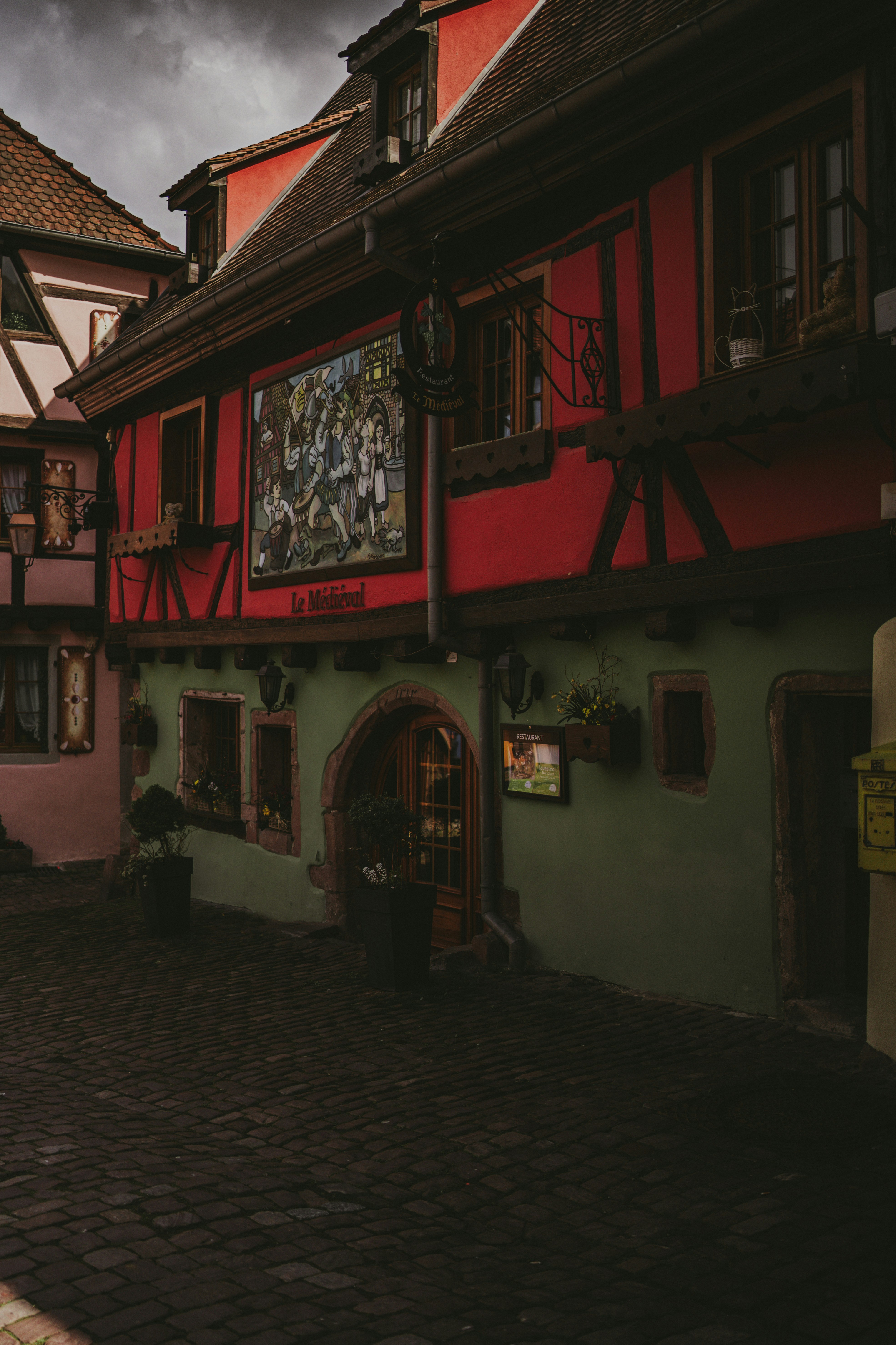 Colorful building with a mural in a quaint village square, featuring rustic architecture and cobblestone paths.