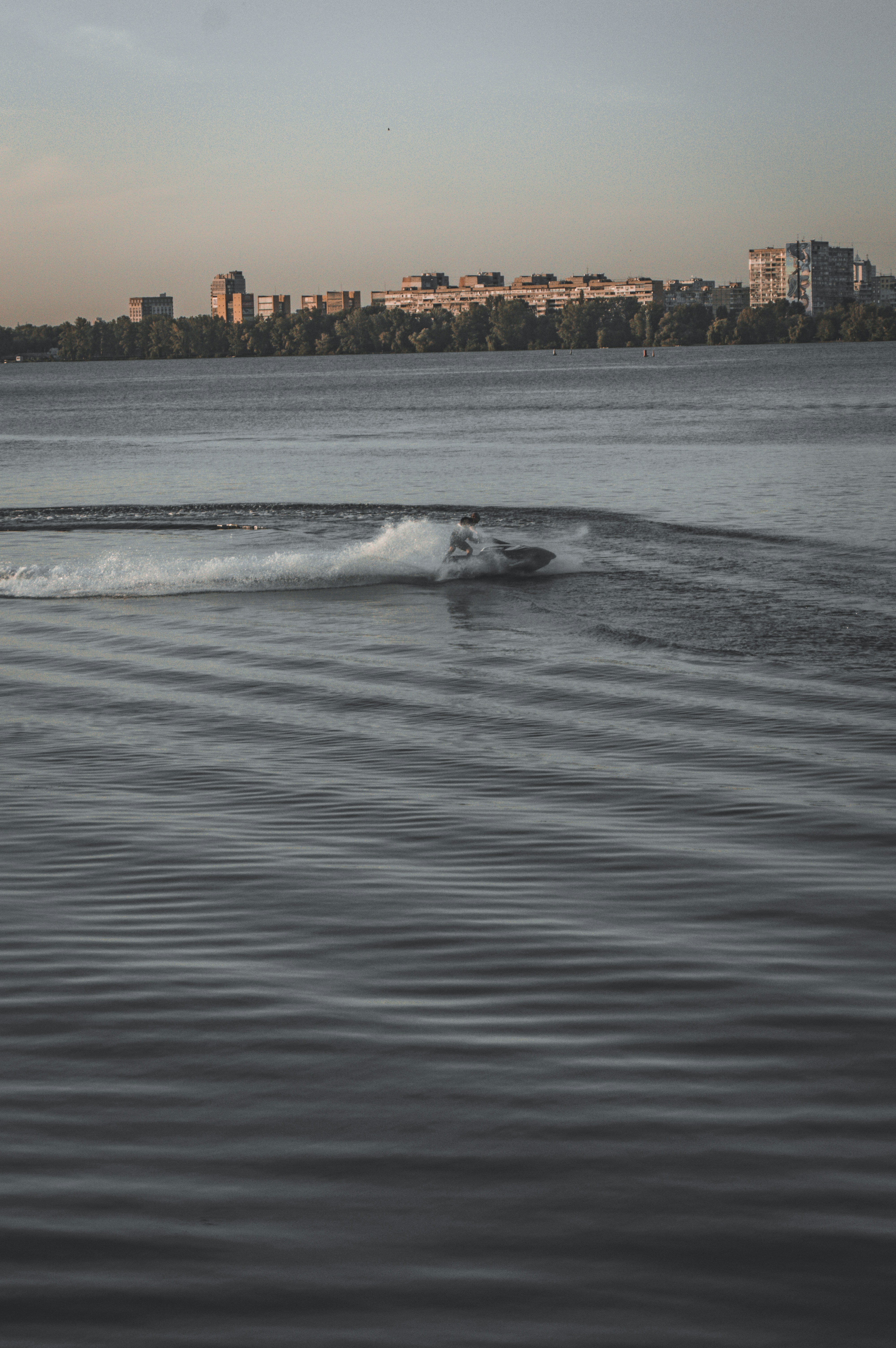 Harbor Glide: a lone surfer tracing a white-foamed wake along a calm urban lake