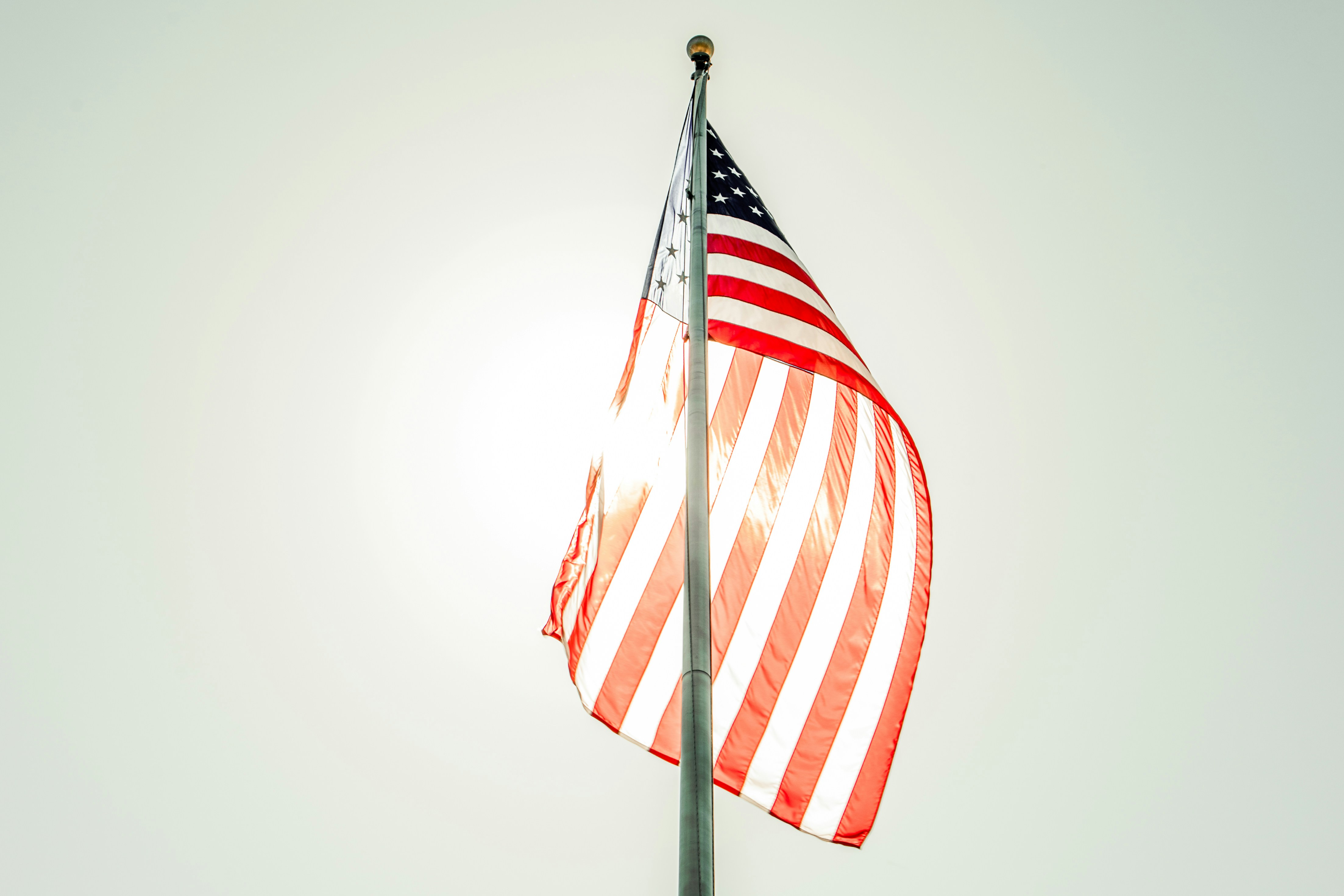 American flag billowing against a bright backdrop, illuminated by sunlight.