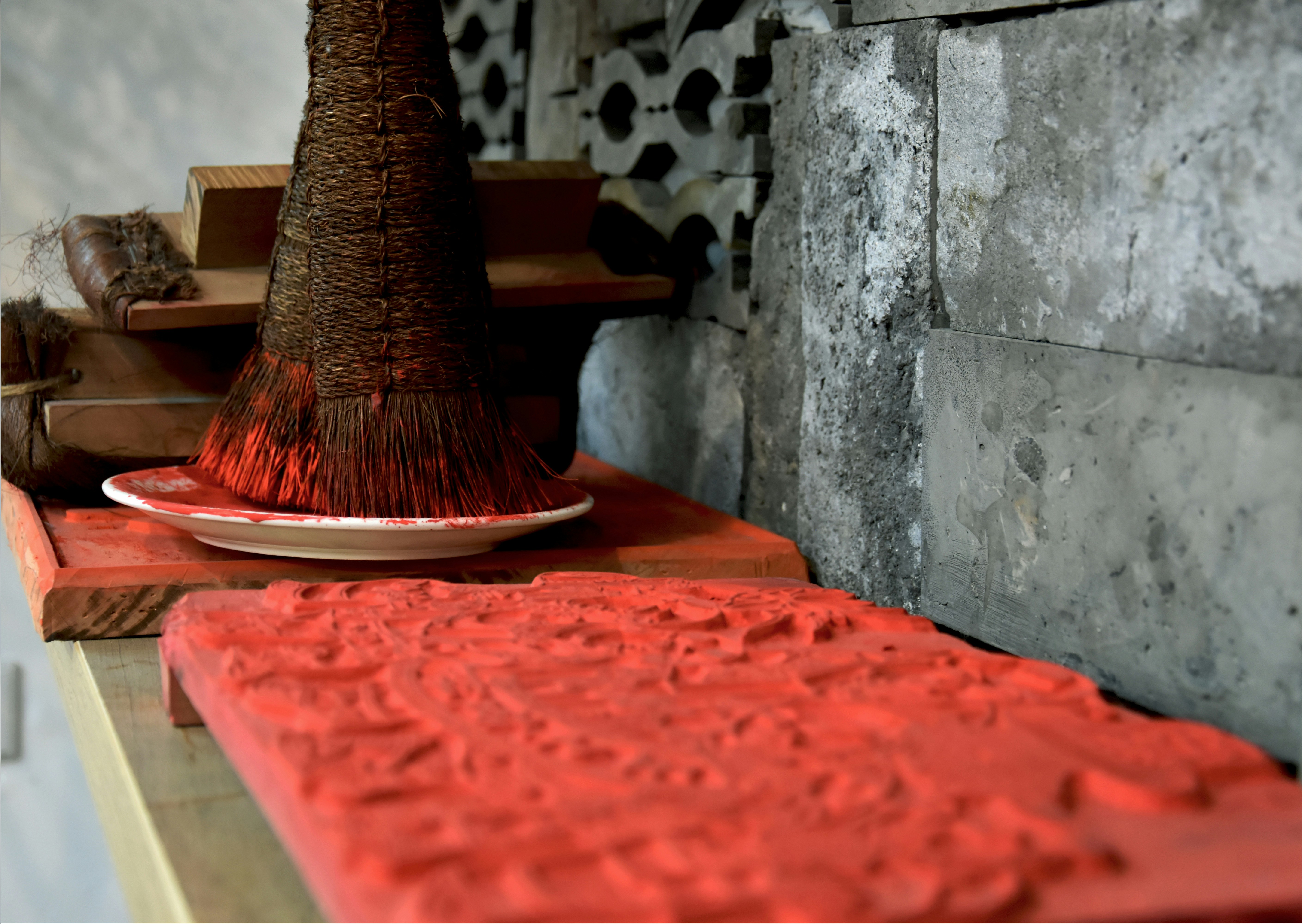 Intricately carved red block and traditional brush resting on a wooden surface, surrounded by textured stone walls.
