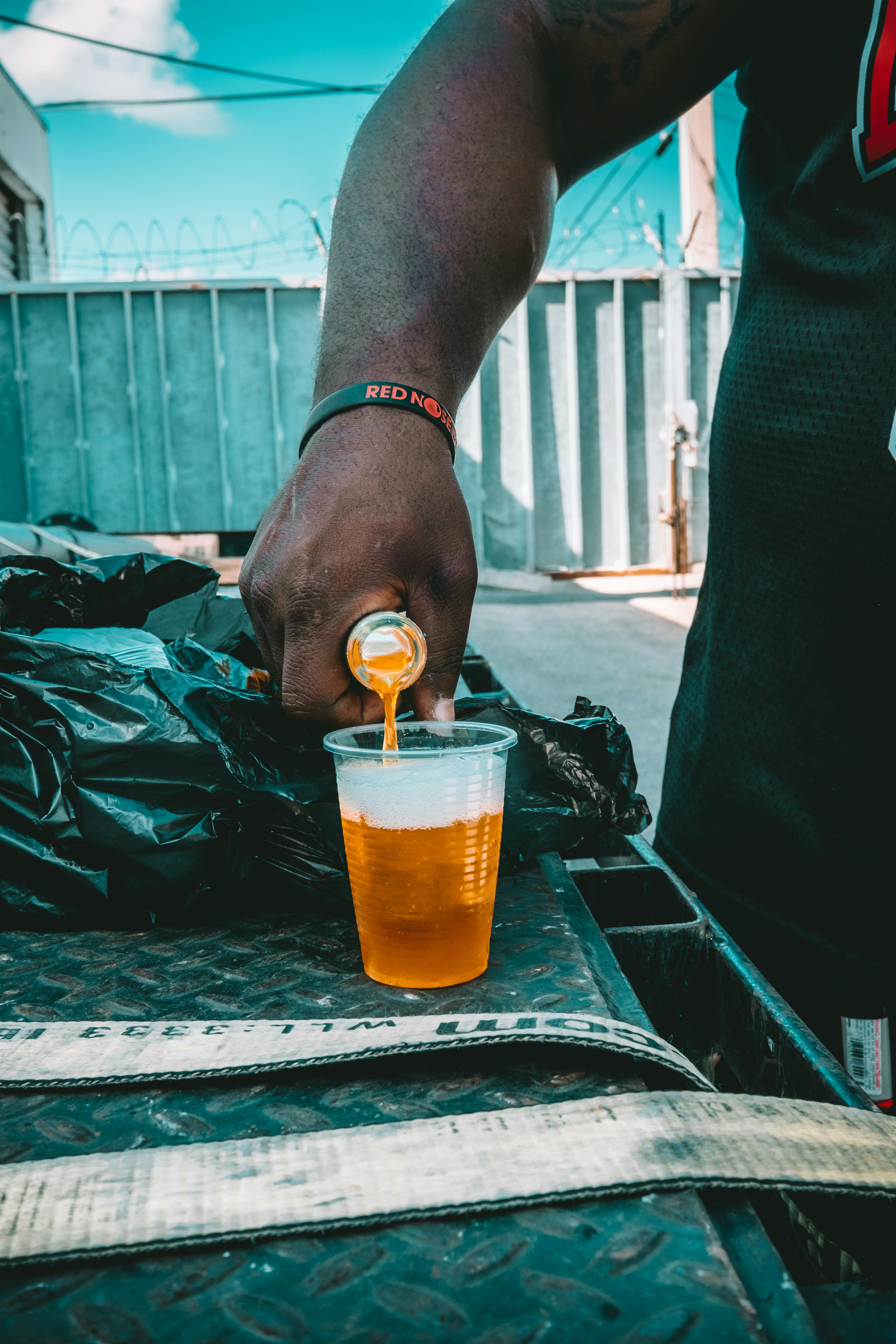 Amber Gravity on Steel: a hand pours beer into a plastic cup in a gritty urban setting