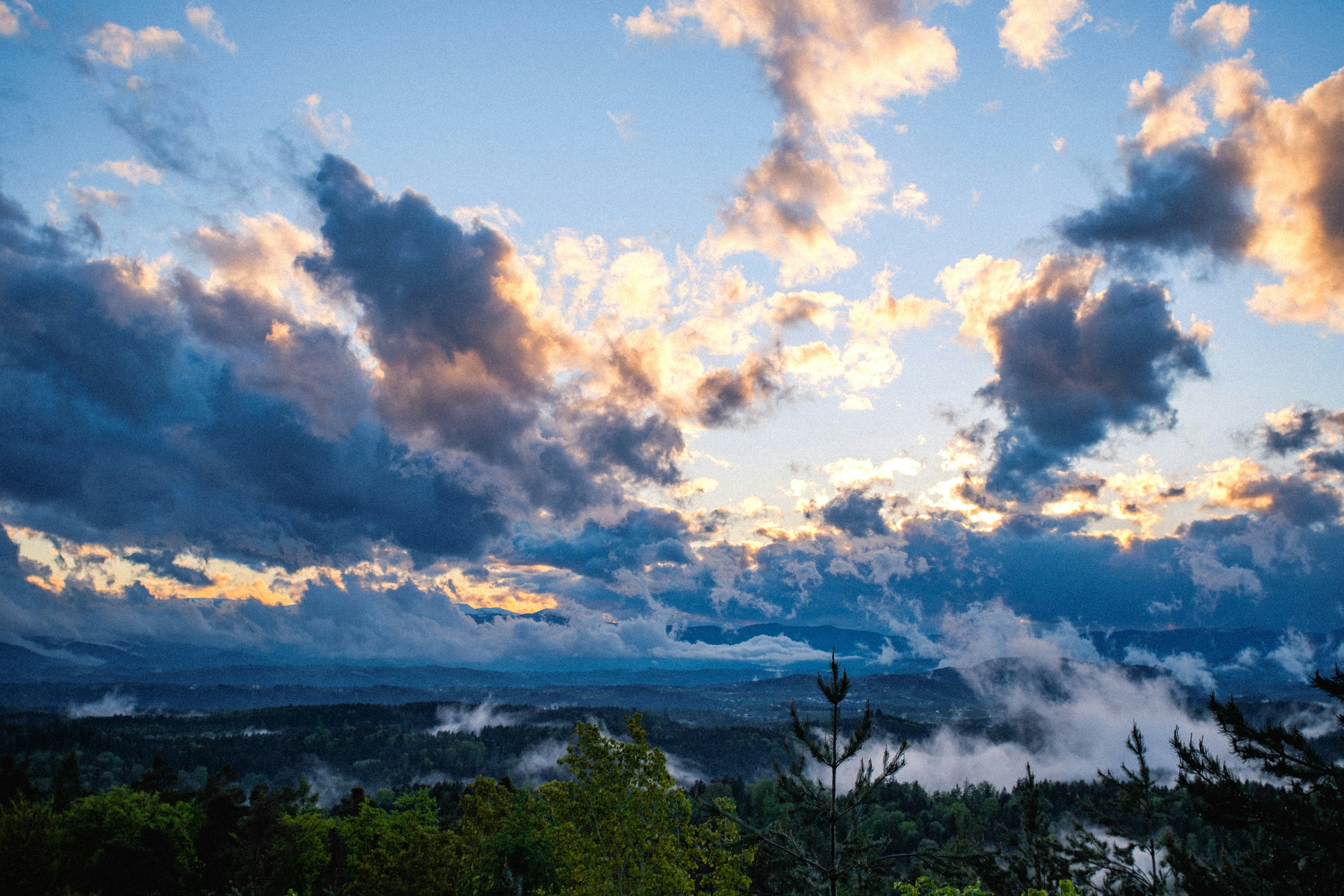 Dramatic clouds illuminated by the setting sun over a mist-covered forest.