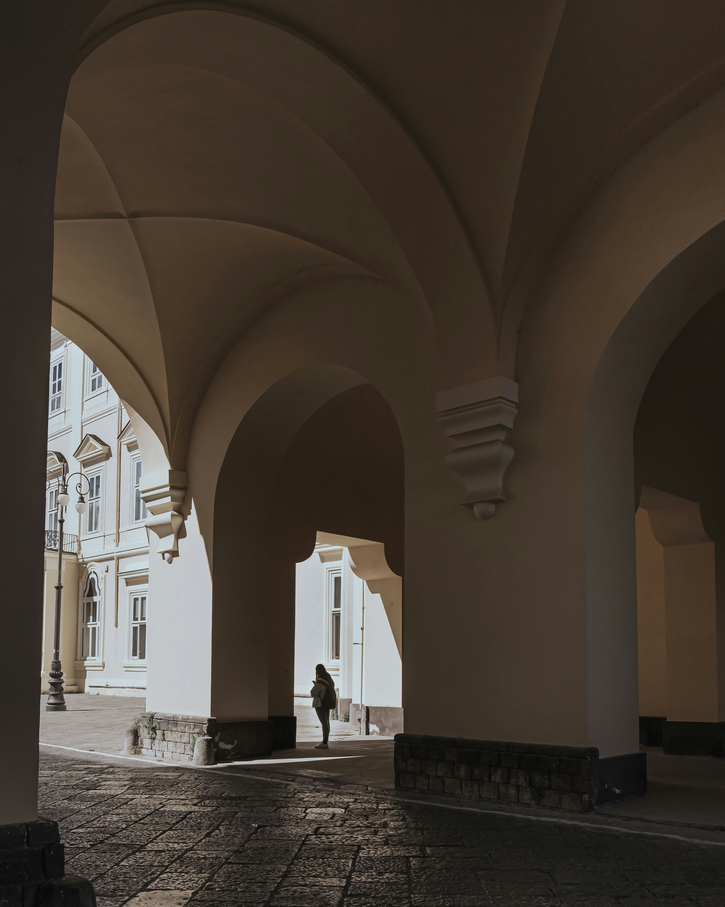 A lone figure walks through a series of grand arches, highlighting the interplay of light and shadow in a historical setting.