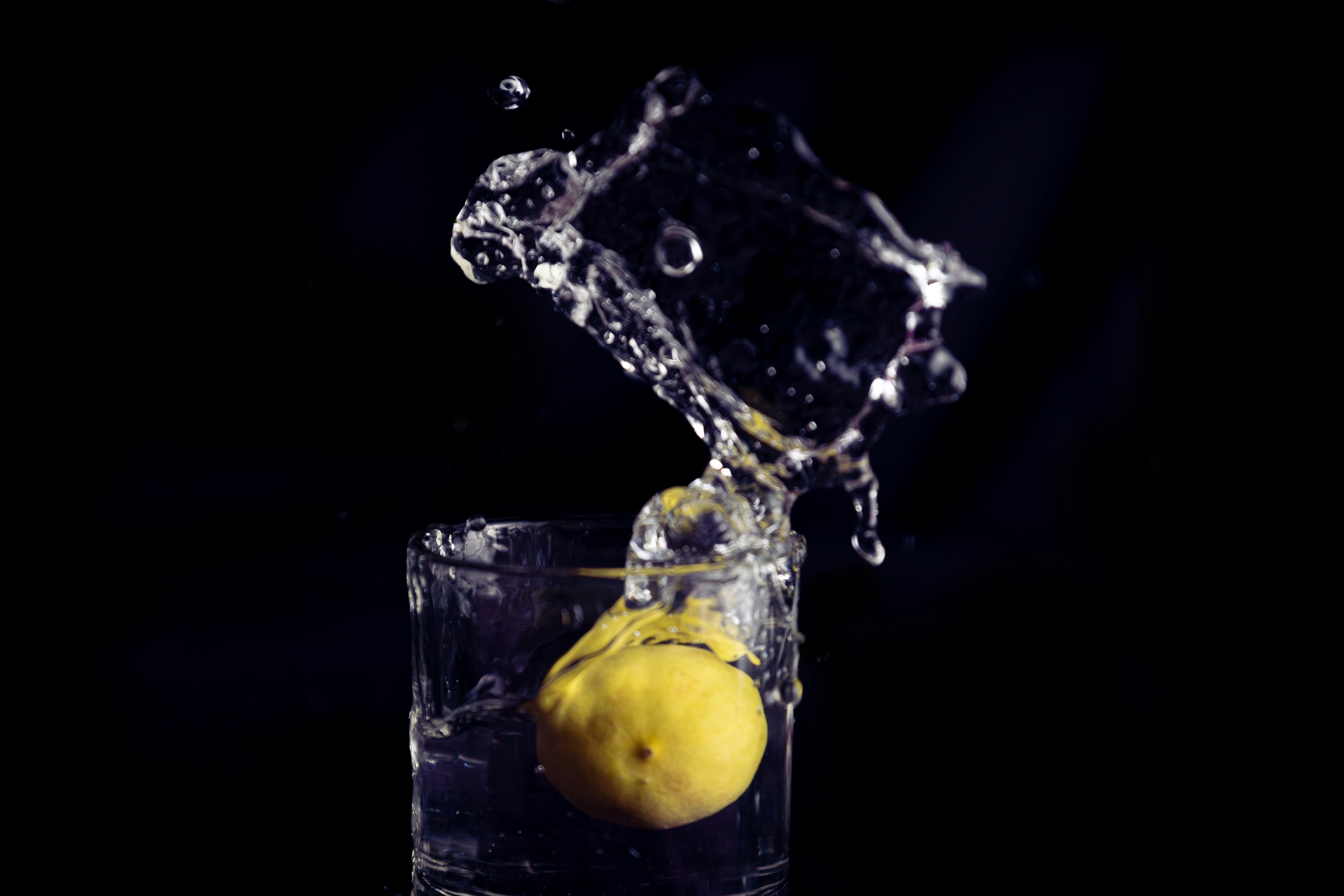 Yellow lemon plunging into a glass of water, creating a dynamic splash against a dark background.