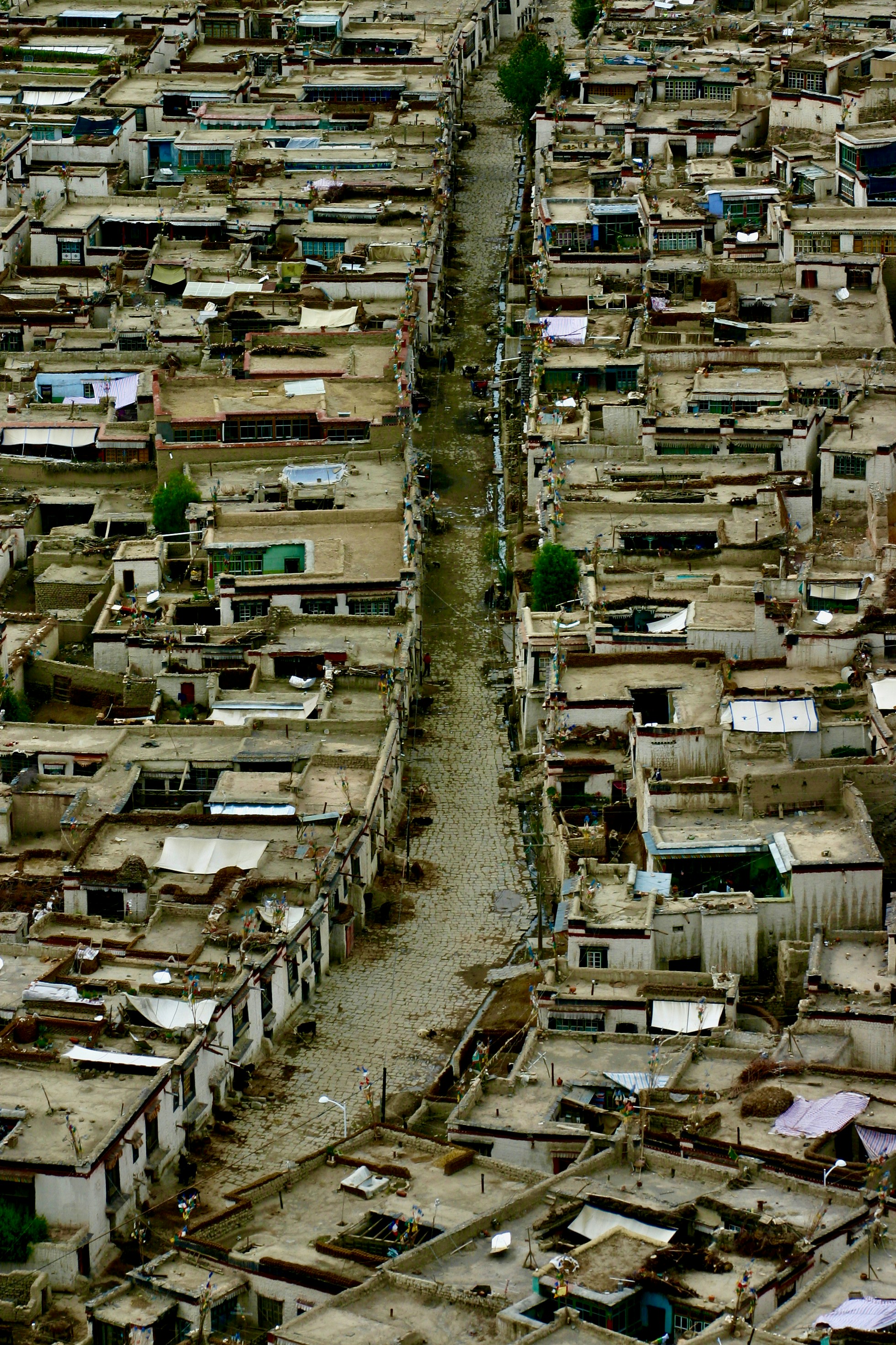 Aerial view of densely packed urban structures with narrow pathways, showcasing the intricate layout of a cityscape. The scene highlights the contrast between buildings and the natural elements interspersed throughout.