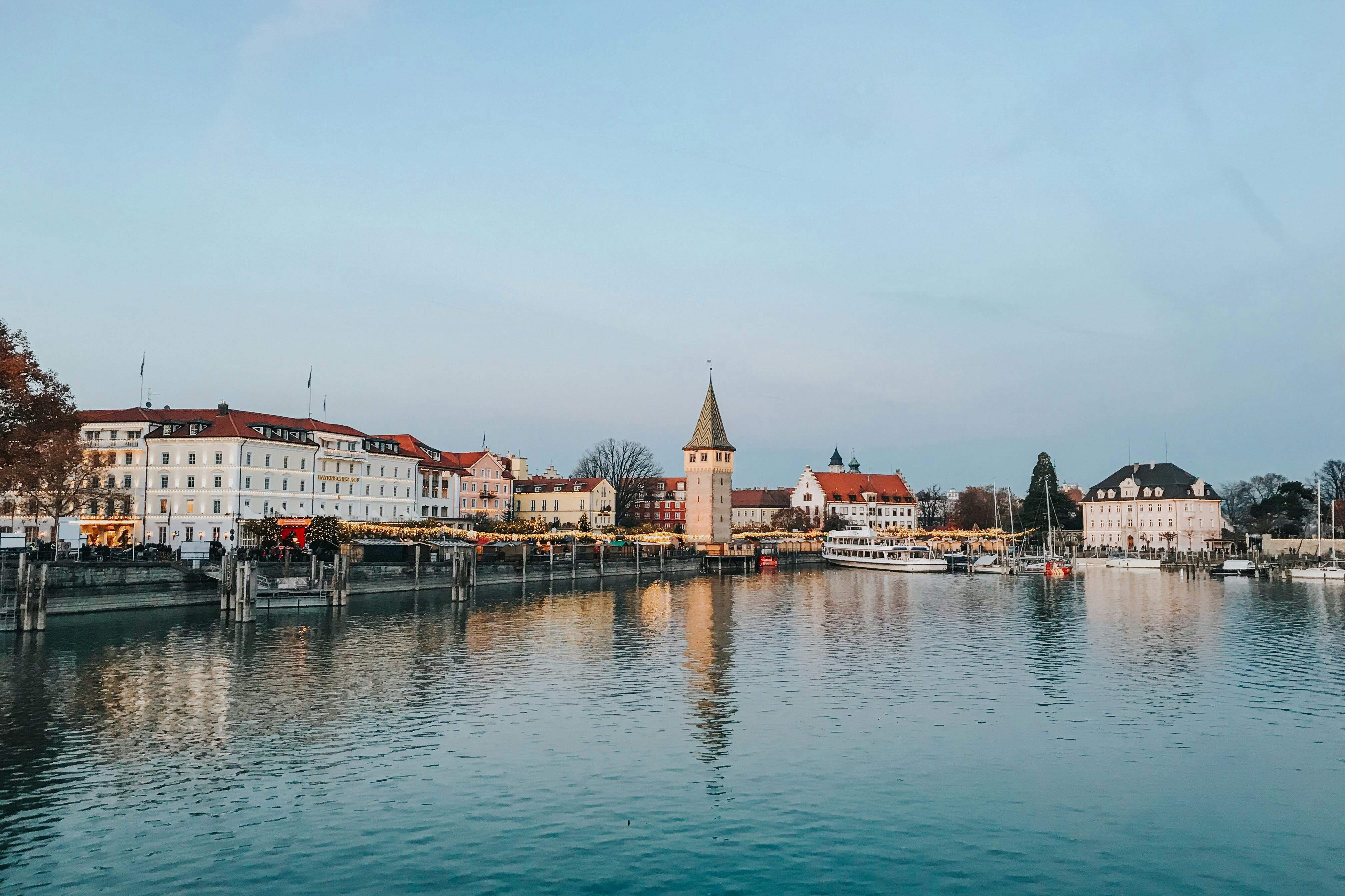 Tranquil waterfront scene with historic buildings reflecting in calm waters under a pastel sky.