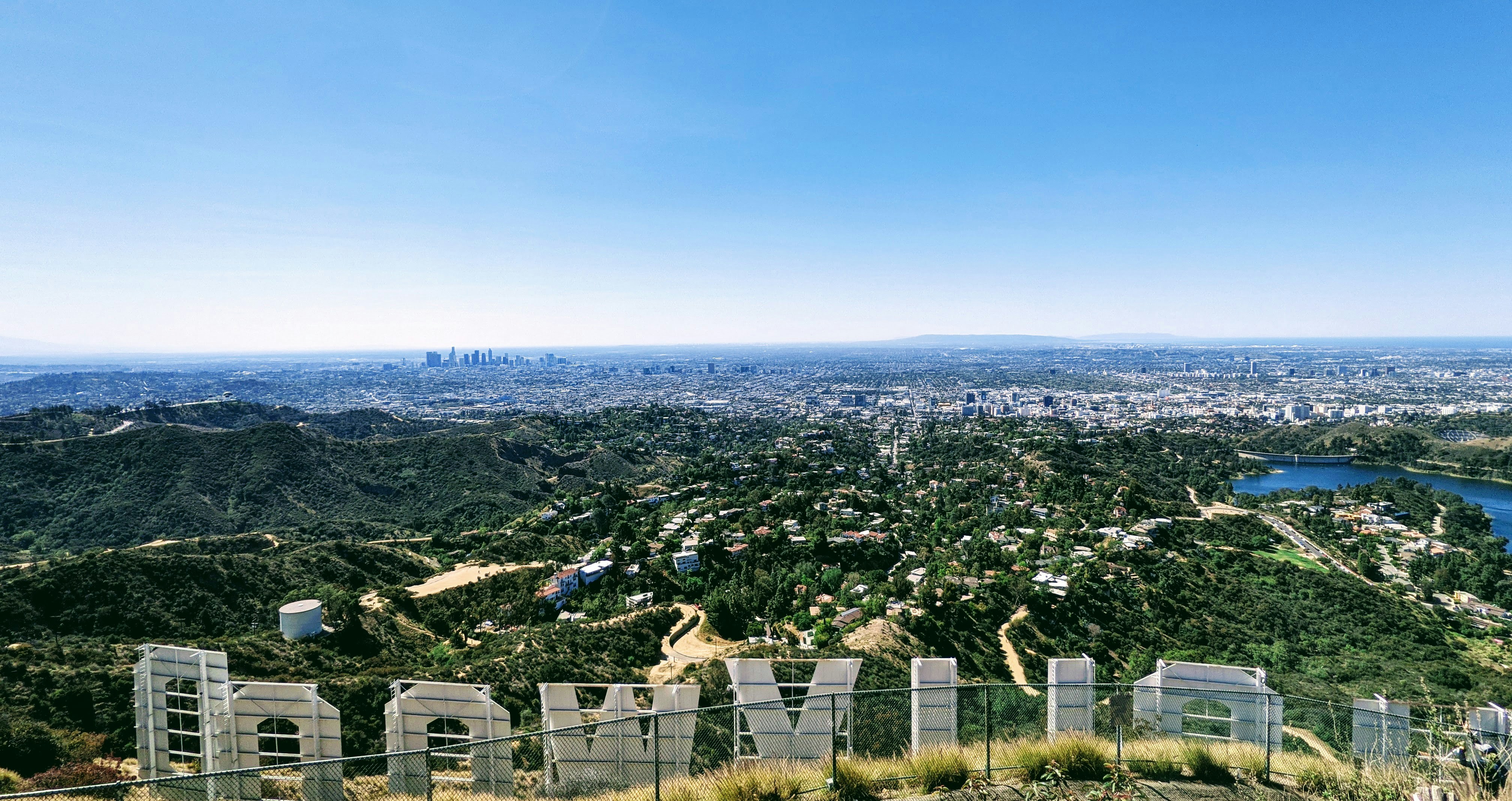Panoramic view of a sprawling cityscape beyond famous hillside letters under a clear blue sky.