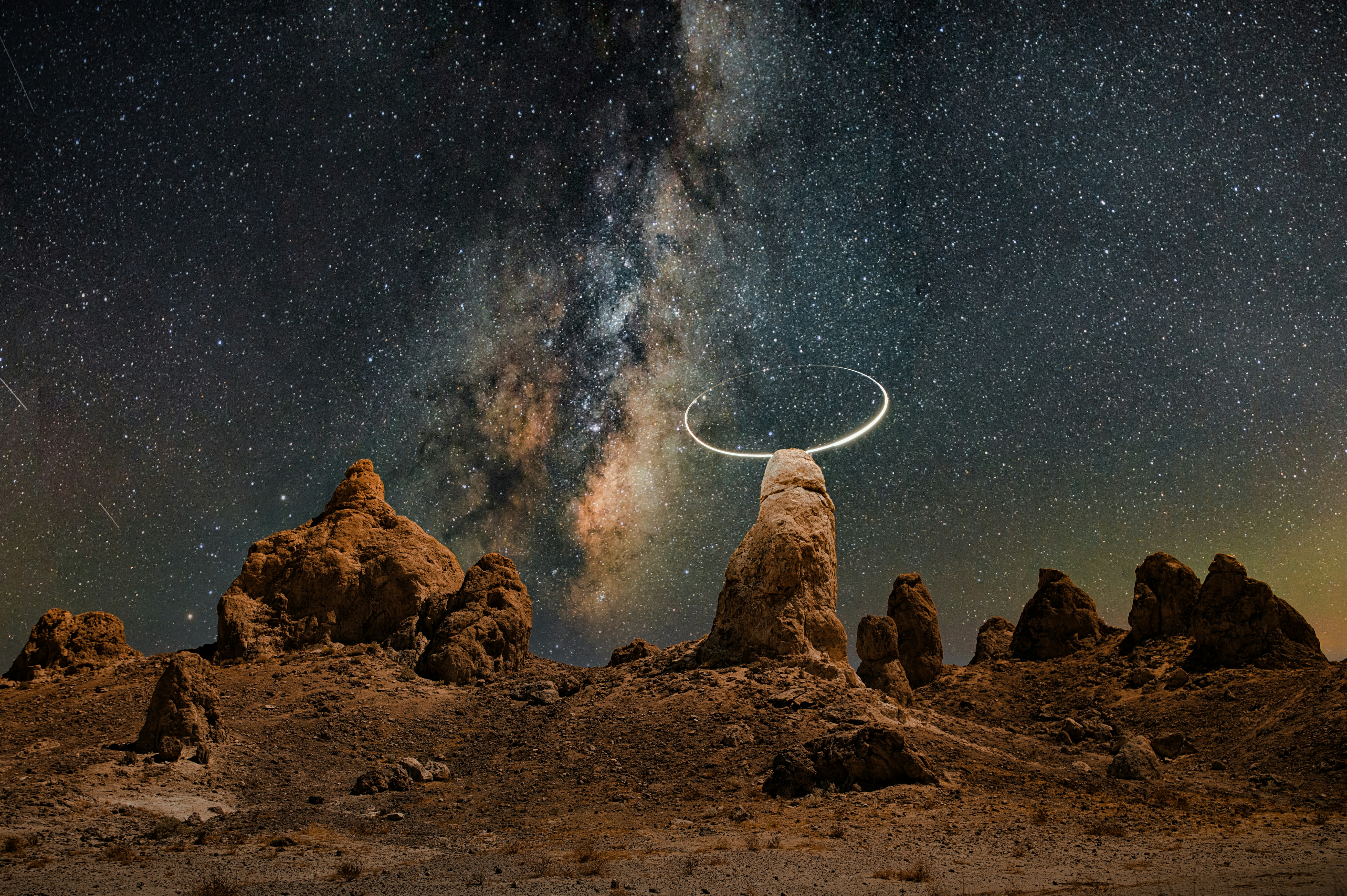 Eerie rock formations silhouetted against a vibrant Milky Way, with a luminescent halo encircling a prominent peak.