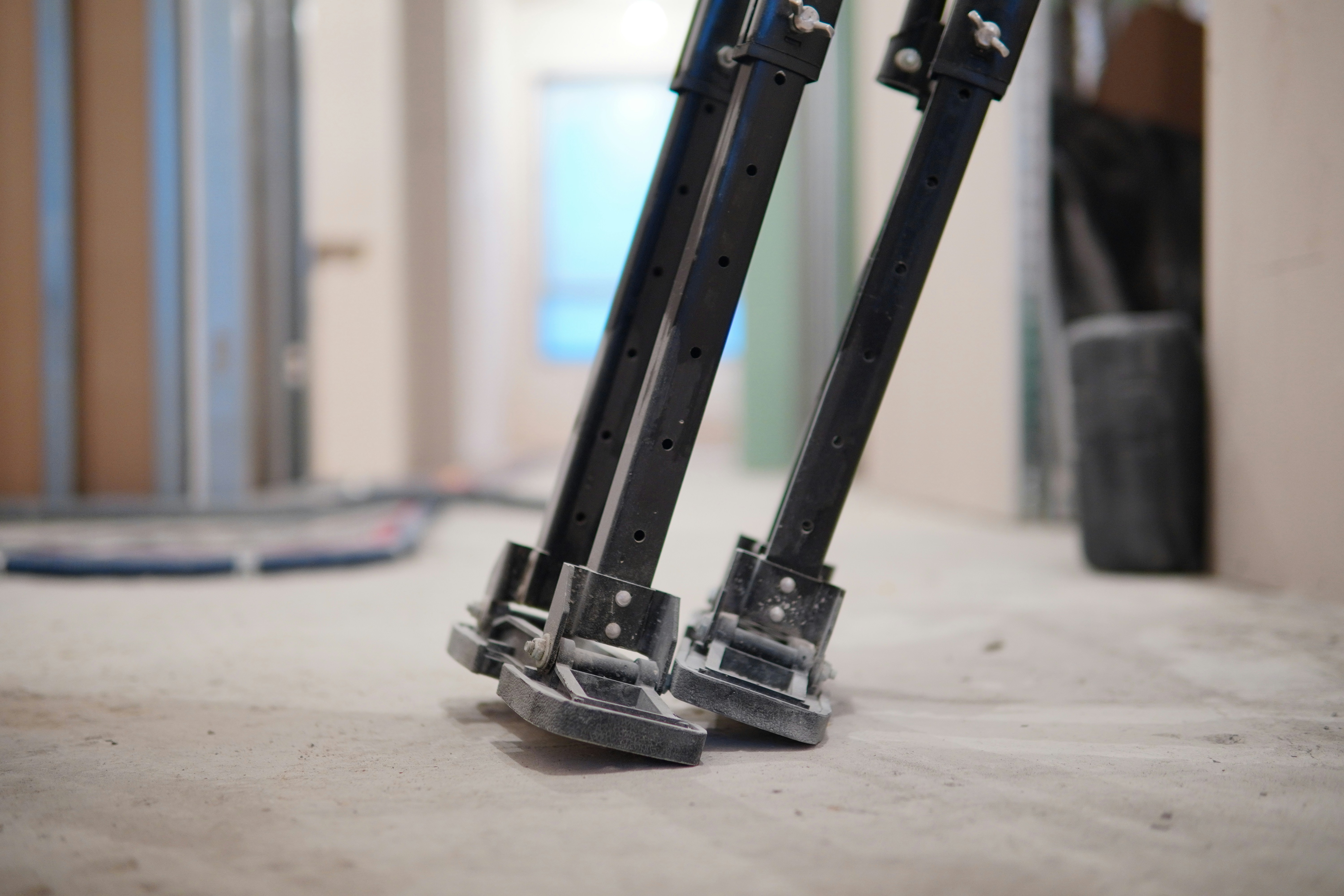 Close-up of adjustable construction legs positioned on a concrete floor, showcasing industrial design and functionality.