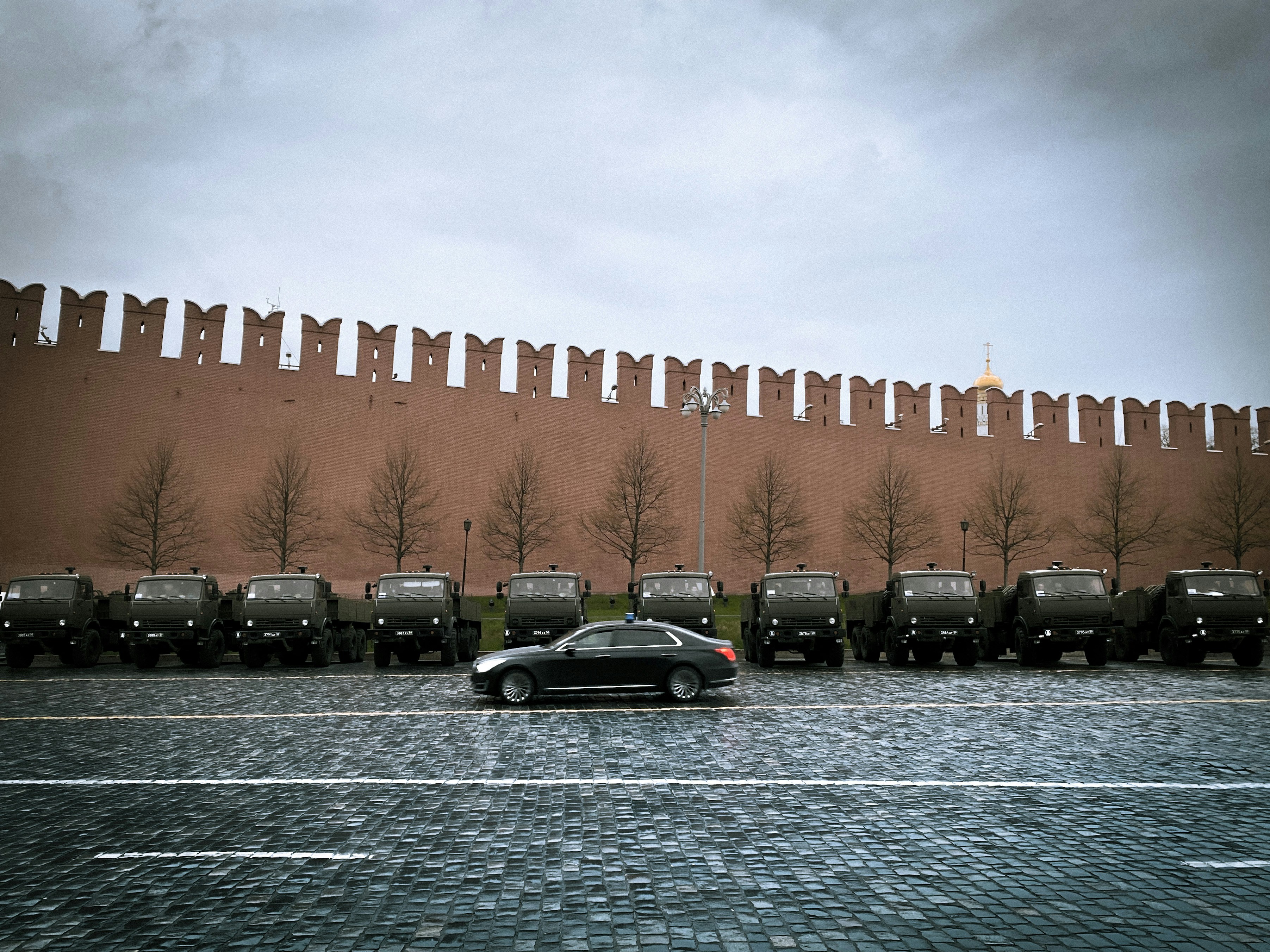 Sedan at the Fortress Gate: A Black Car Before a Line of Military Trucks