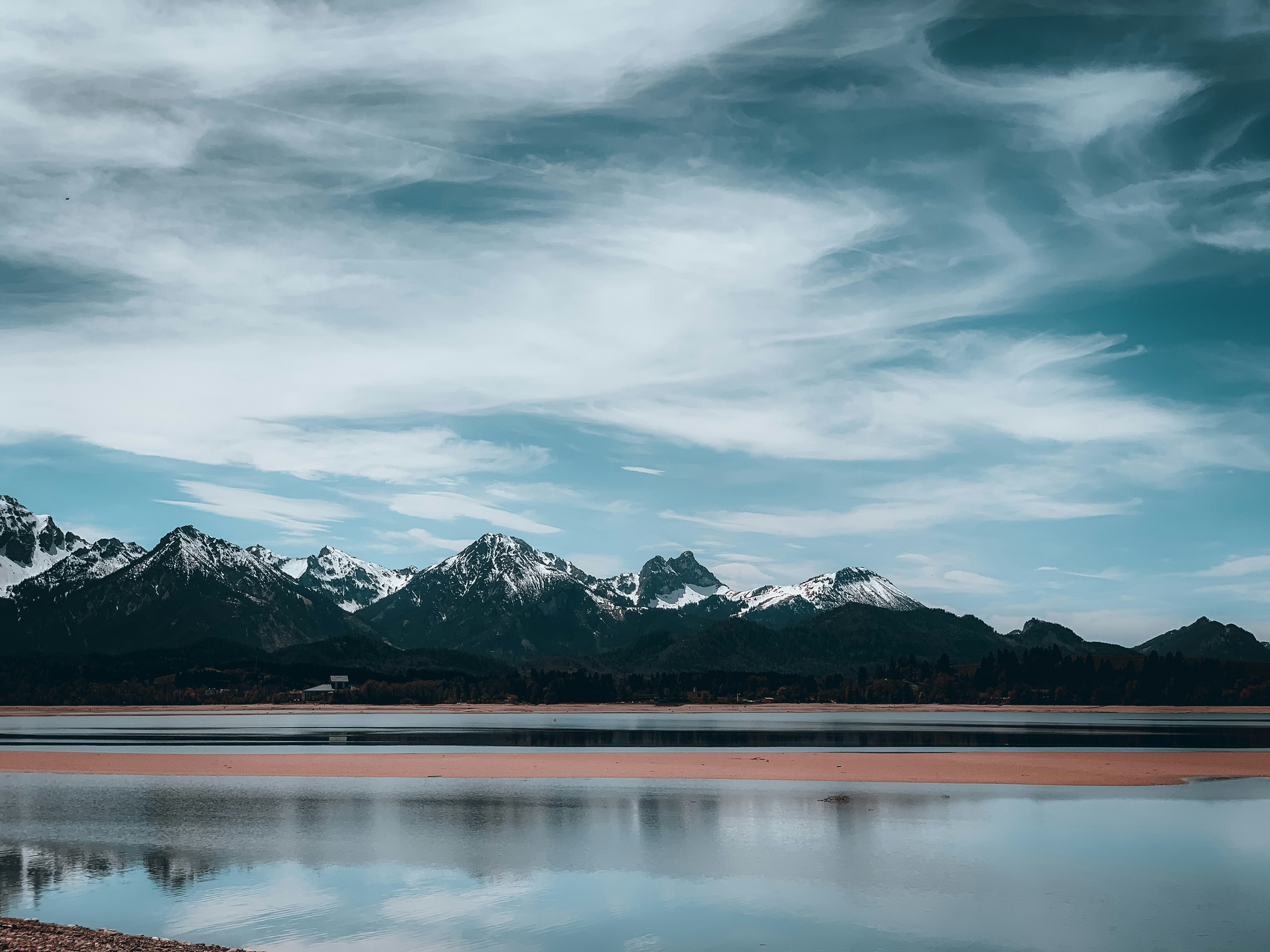 Snow-capped mountains mirrored in a tranquil lake under swirling clouds.