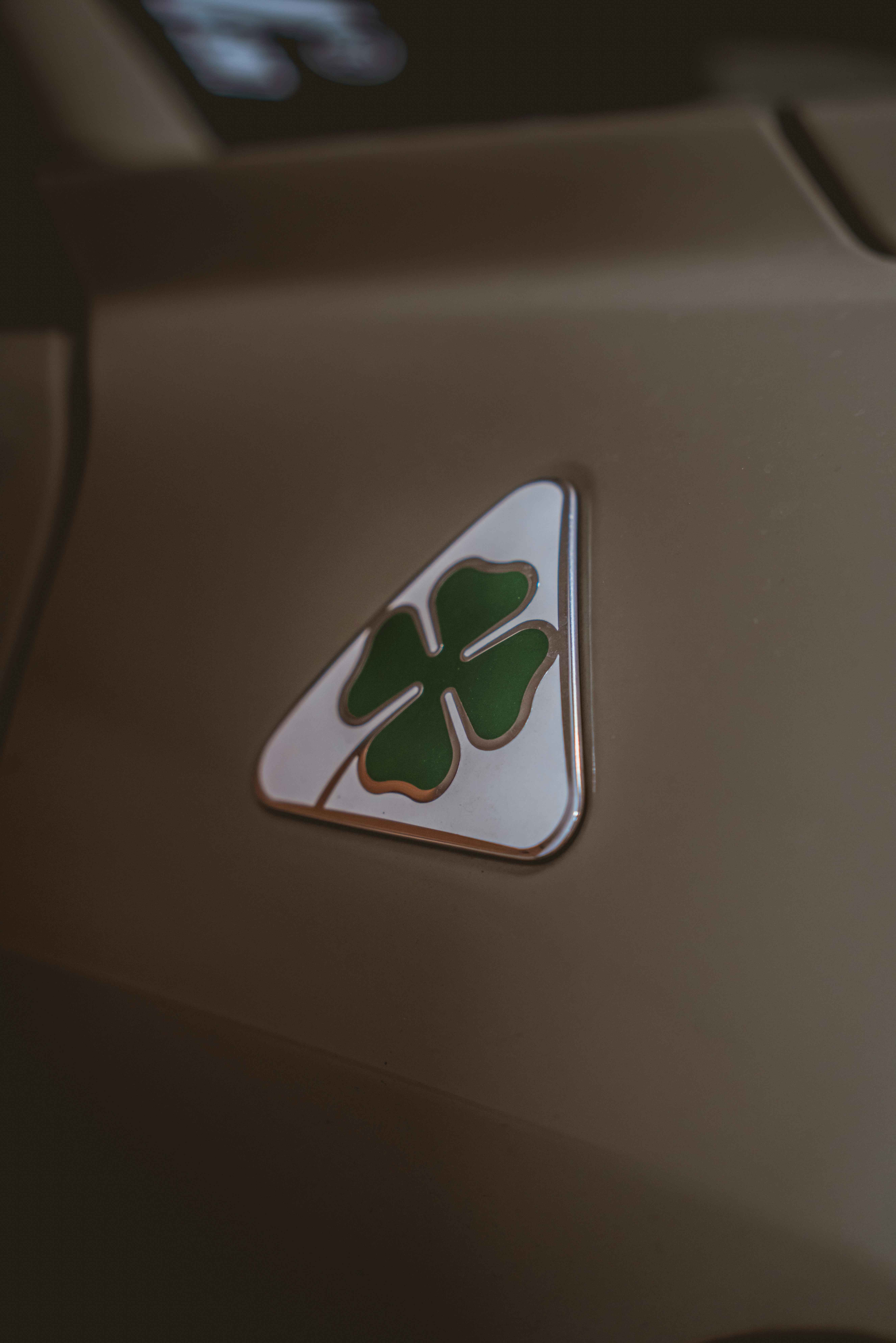 Close-up of a four-leaf clover emblem set against a muted background, highlighting its glossy finish and intricate design.