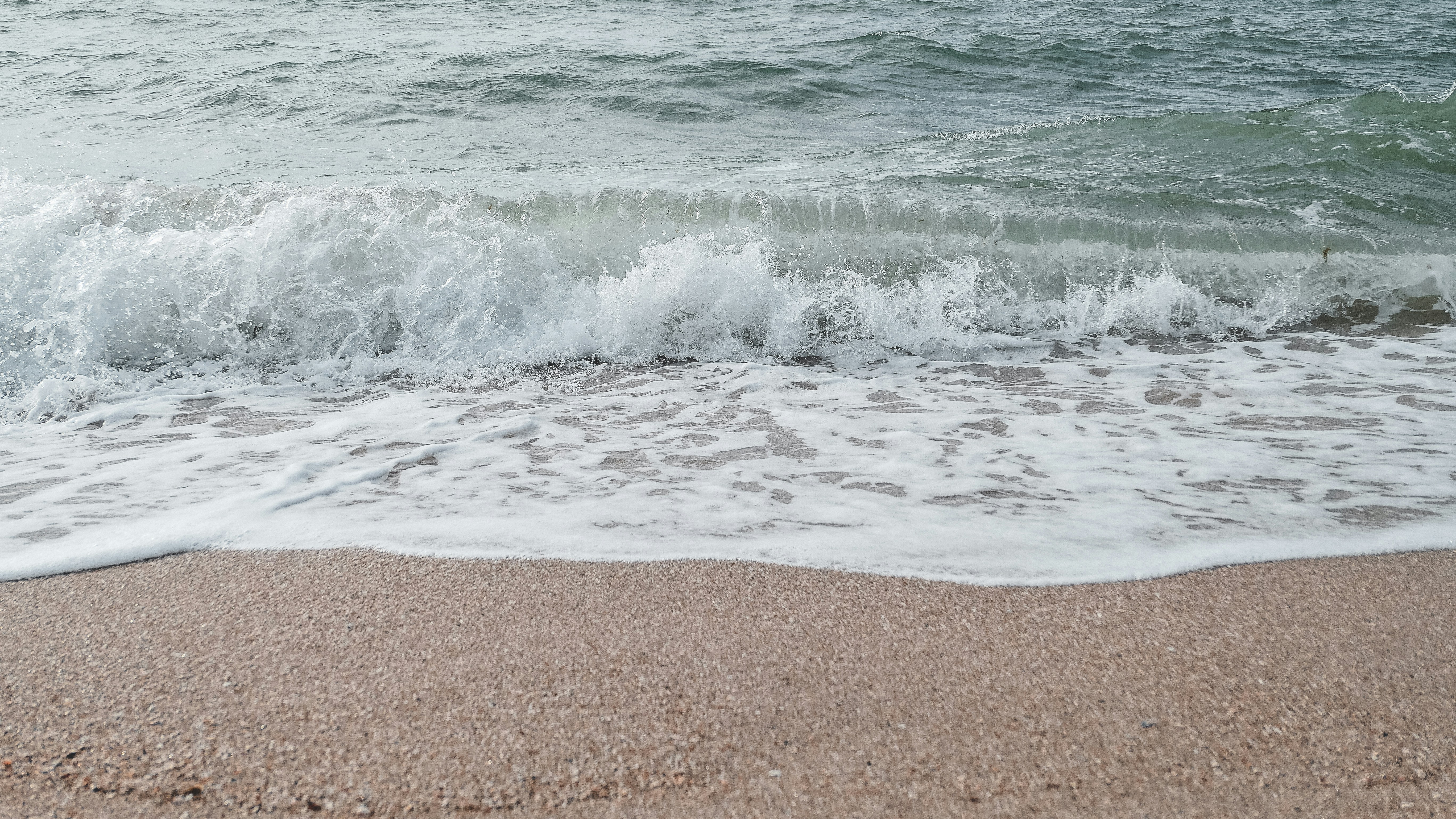 Gentle waves lapping against a sandy shore under a soft, overcast sky.