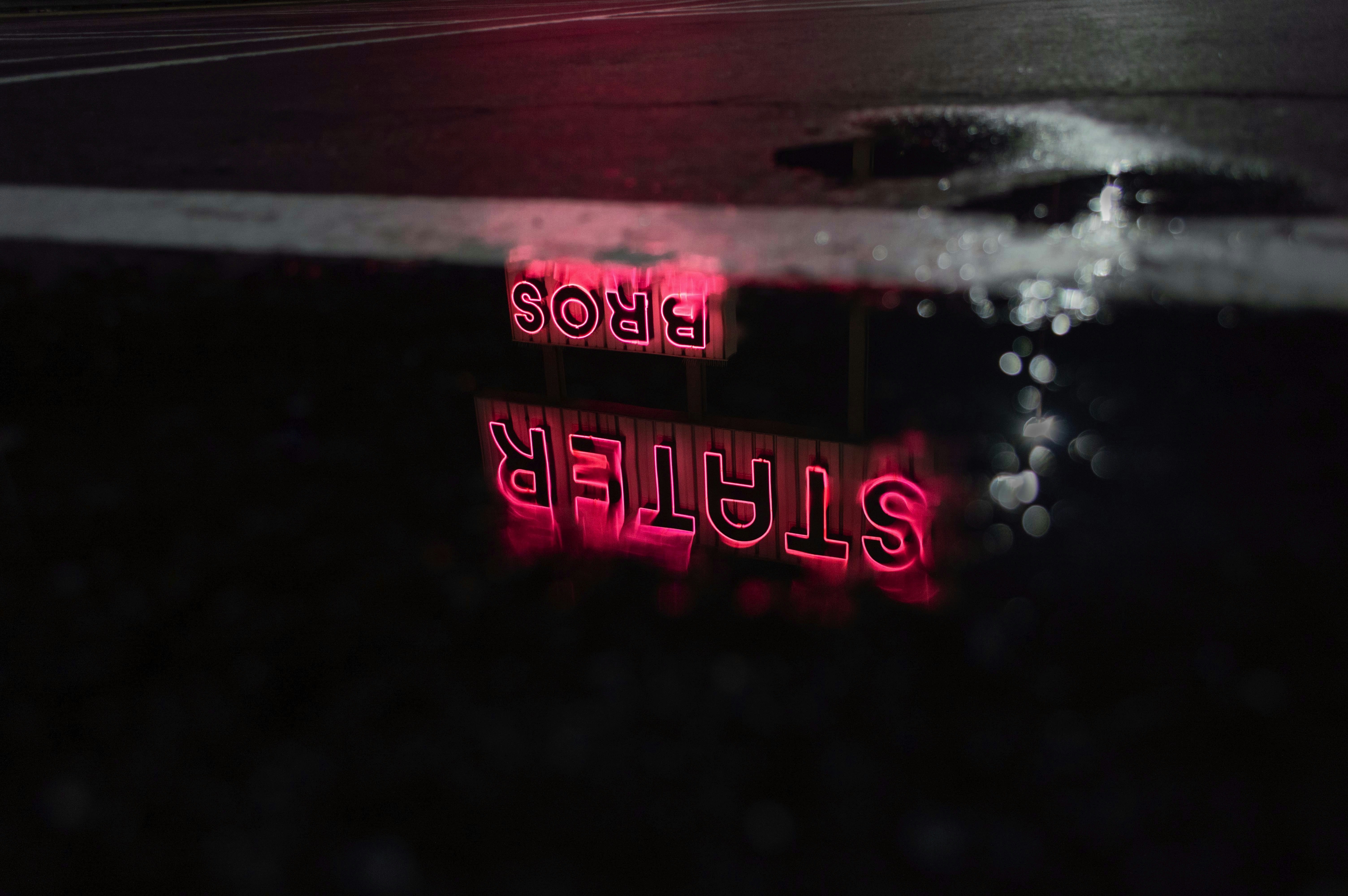 Neon sign reading 'STALTER BROS' reflected in a puddle on a wet surface, capturing the essence of urban nightlife.
