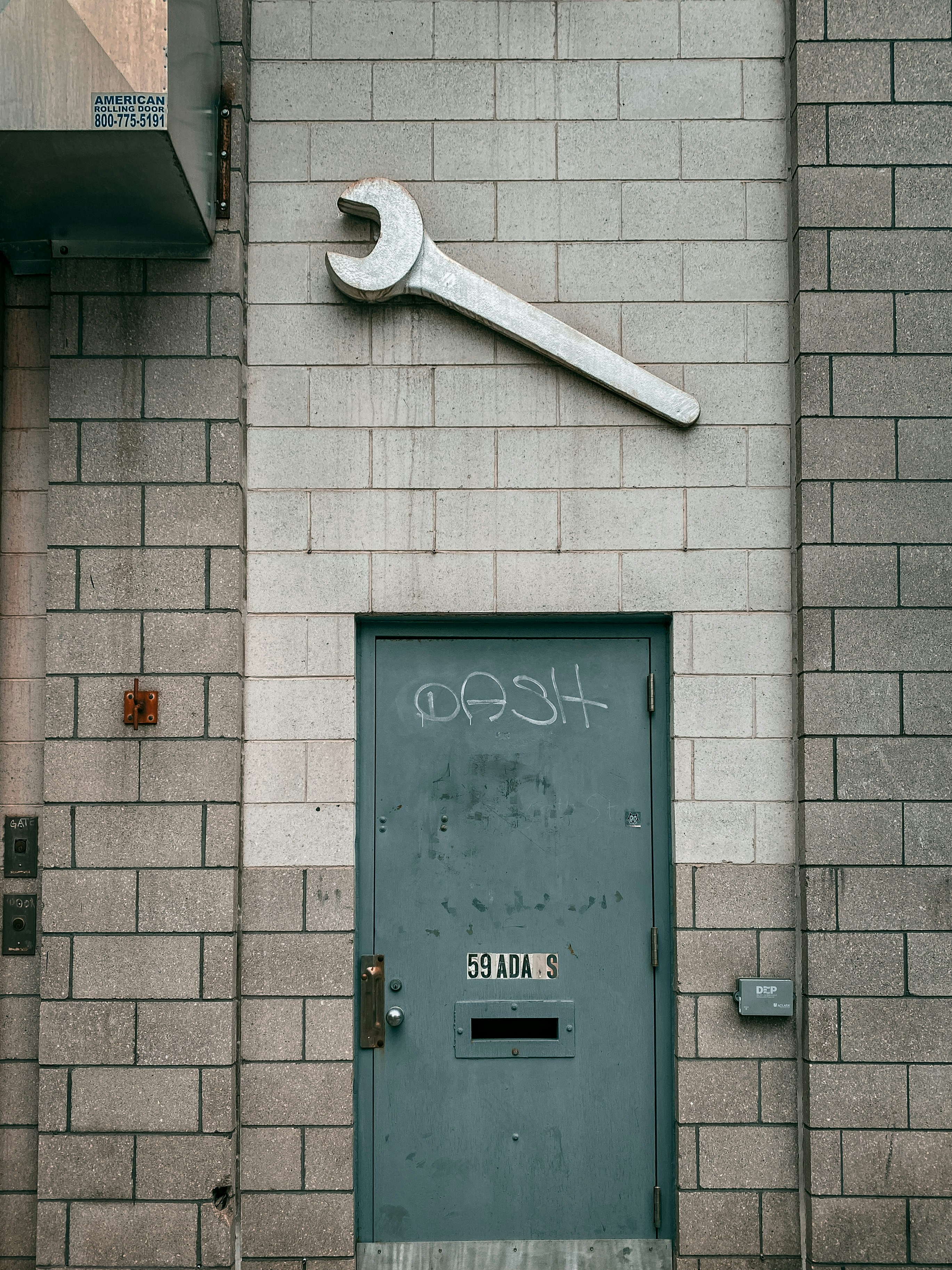 Industrial Wrench Over a Weathered Blue Door in an Urban Brick Facade