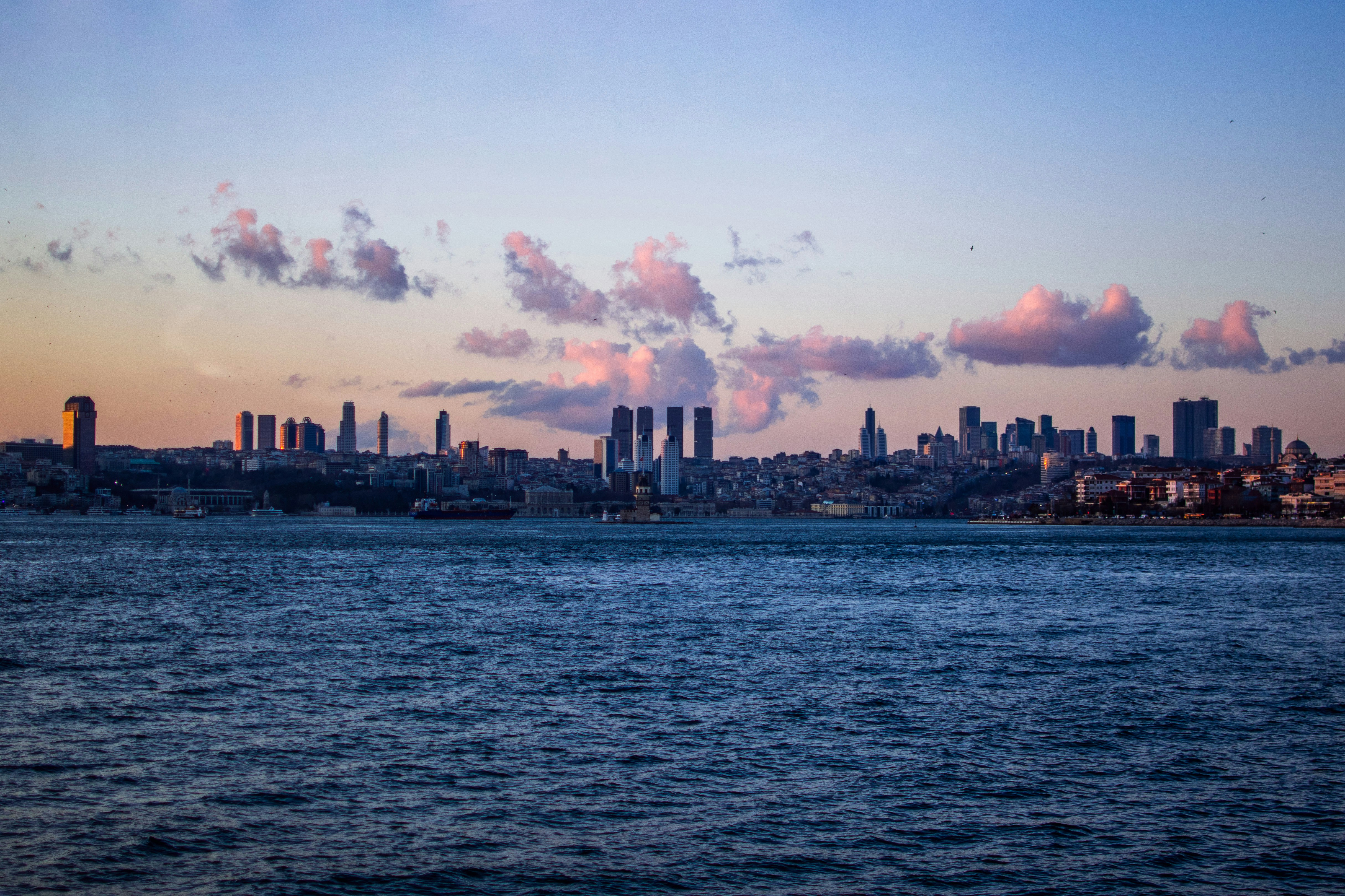 City skyline at dusk with vibrant clouds mirrored in calm waters, showcasing architectural diversity against a colorful sky.