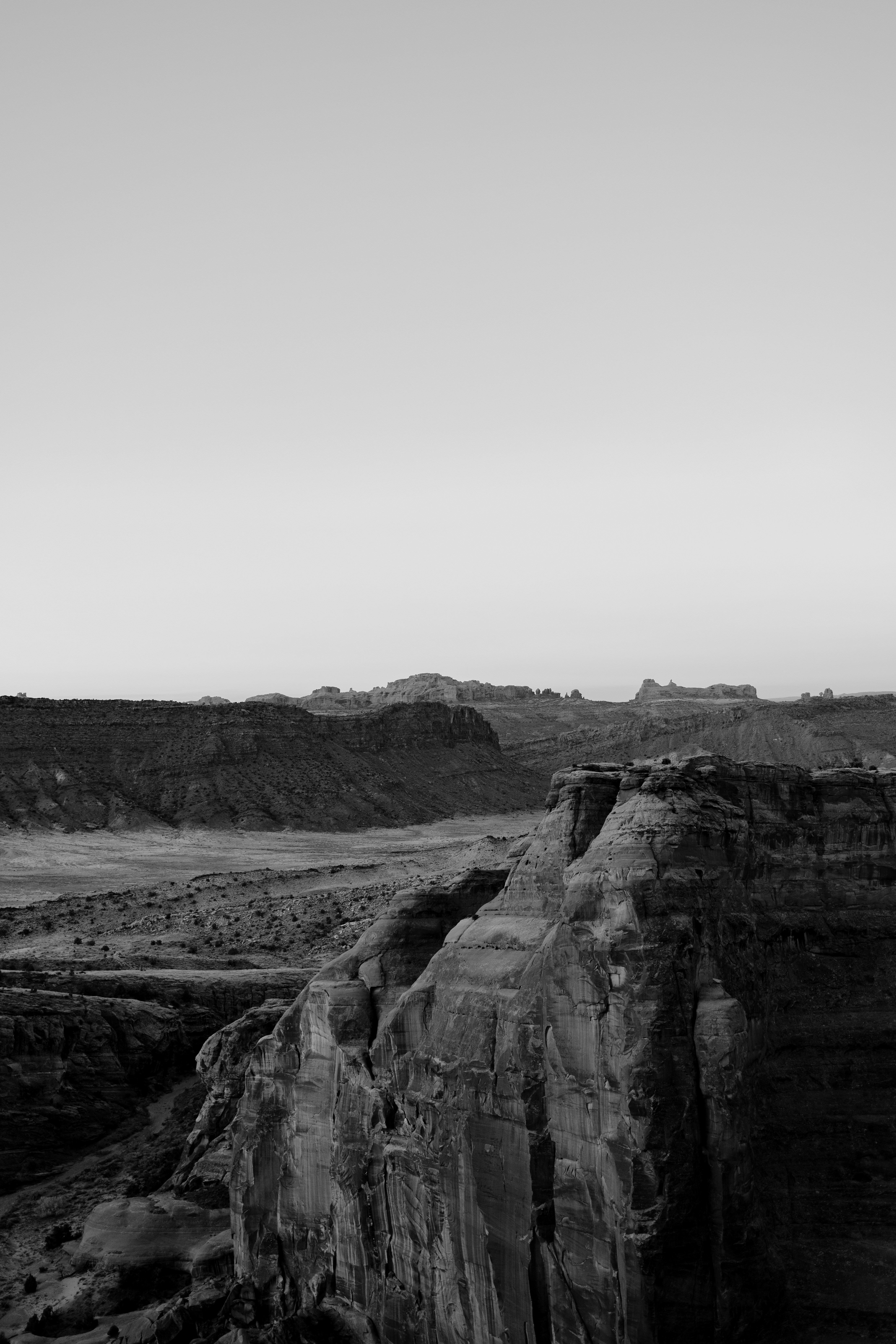 Dramatic cliffs and rugged terrain captured in monochrome, showcasing the stark beauty of a desert landscape at dusk.