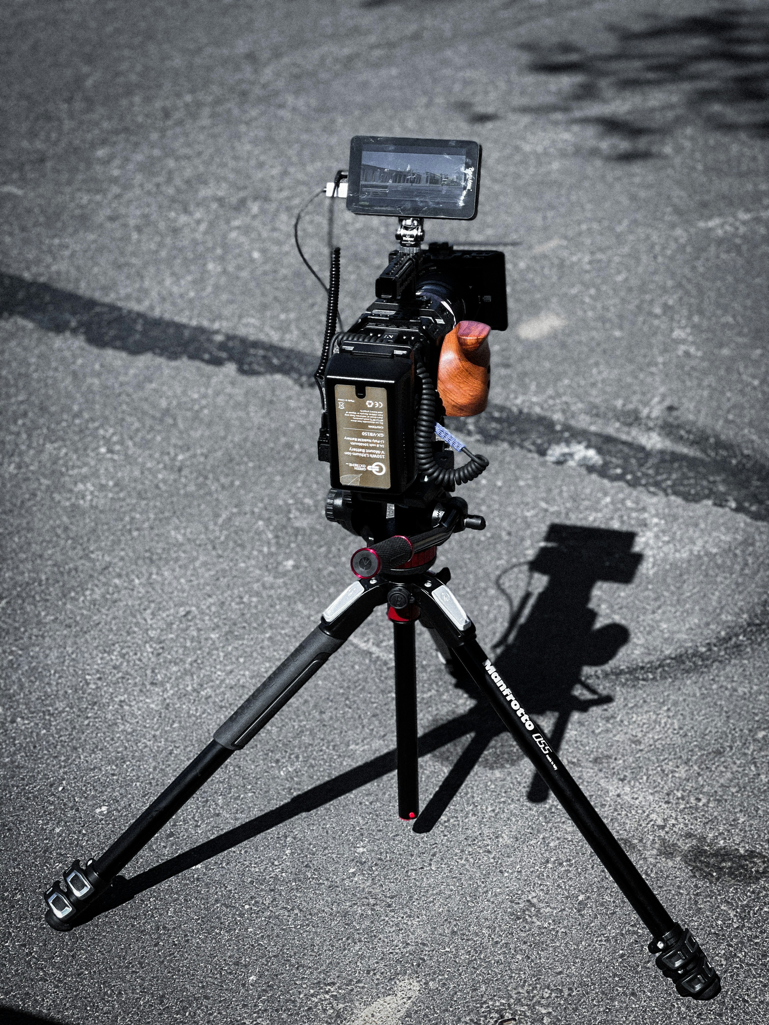 Professional camera setup on a tripod, showcasing an external monitor and intricate controls. The scene emphasizes the equipment's functionality and design.