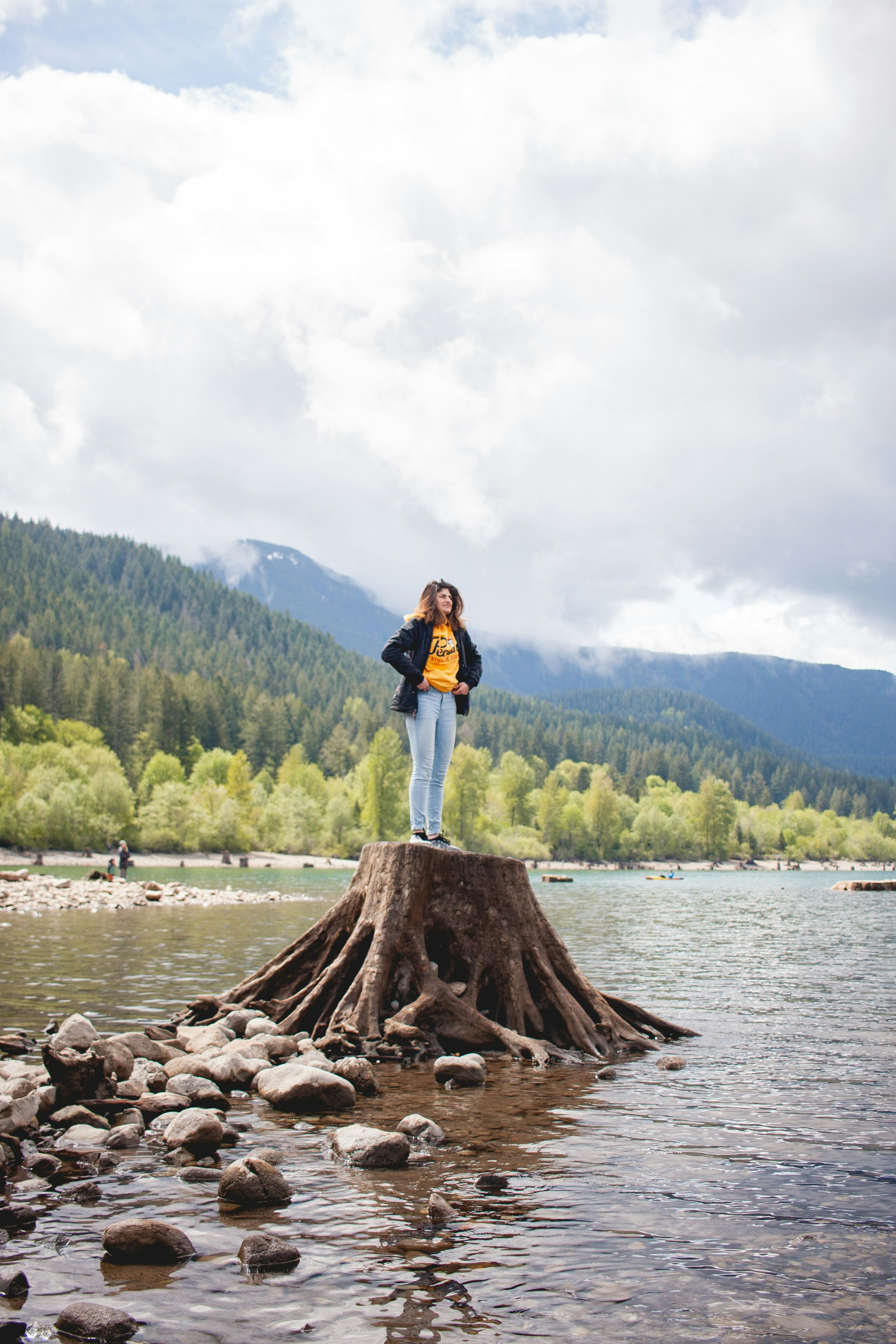 Woman in black jacket standing on brown log near body of water during ...