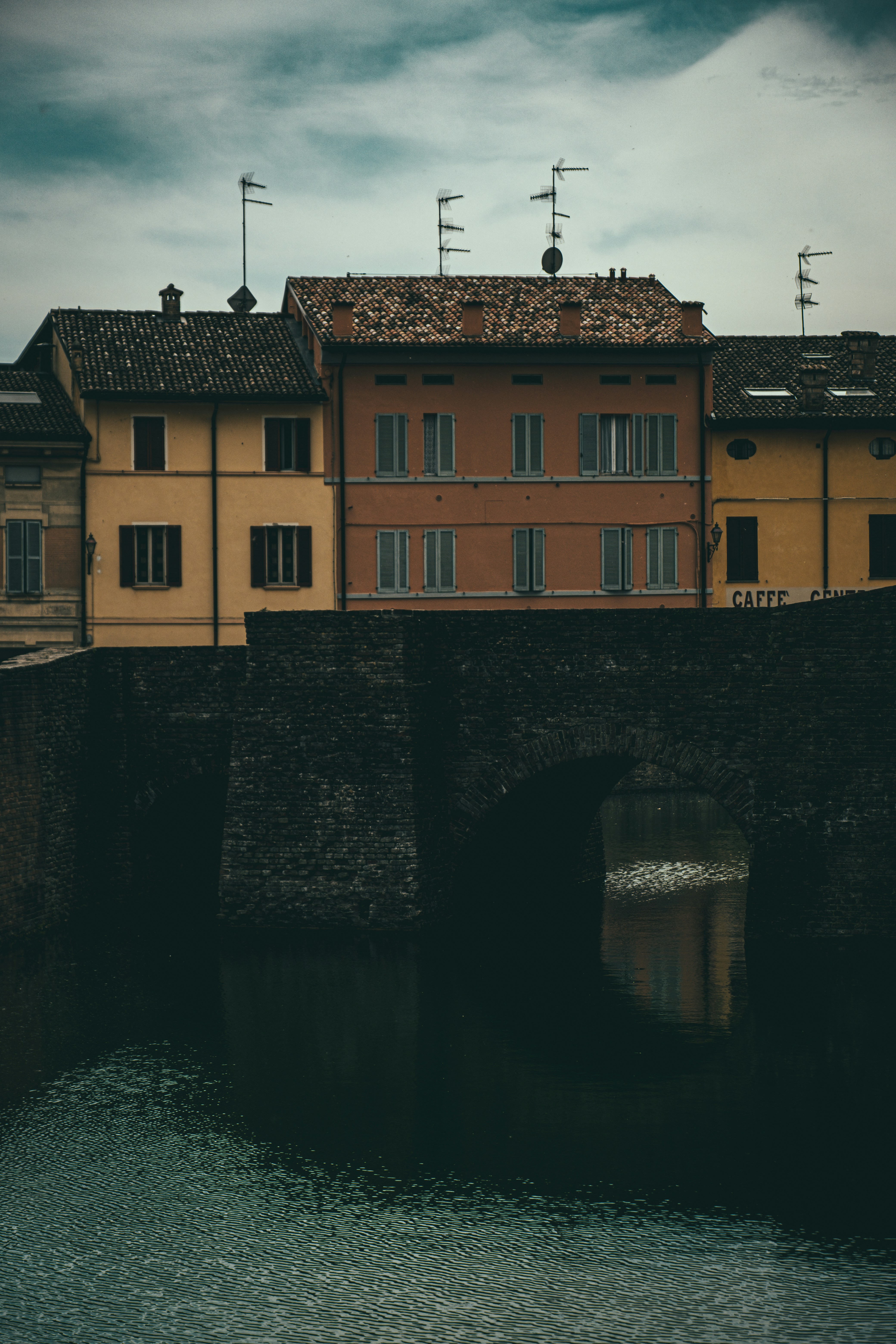 Historic stone bridge arching over a tranquil waterway, flanked by charming buildings with colorful façades. The scene evokes a sense of nostalgia.