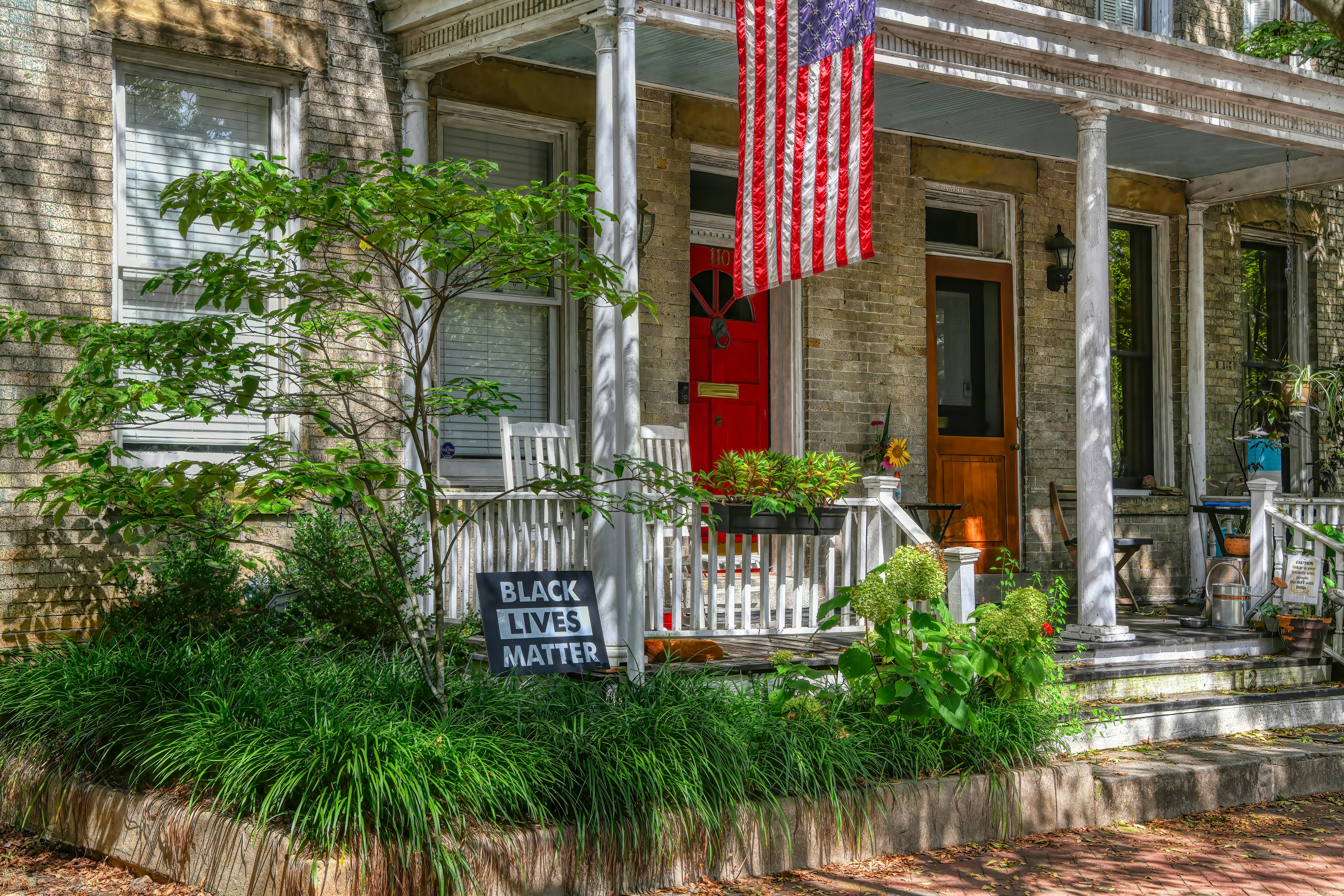 Front porch adorned with greenery, featuring a prominent 'BLACK LIVES MATTER' sign and an American flag, reflecting community spirit and advocacy.