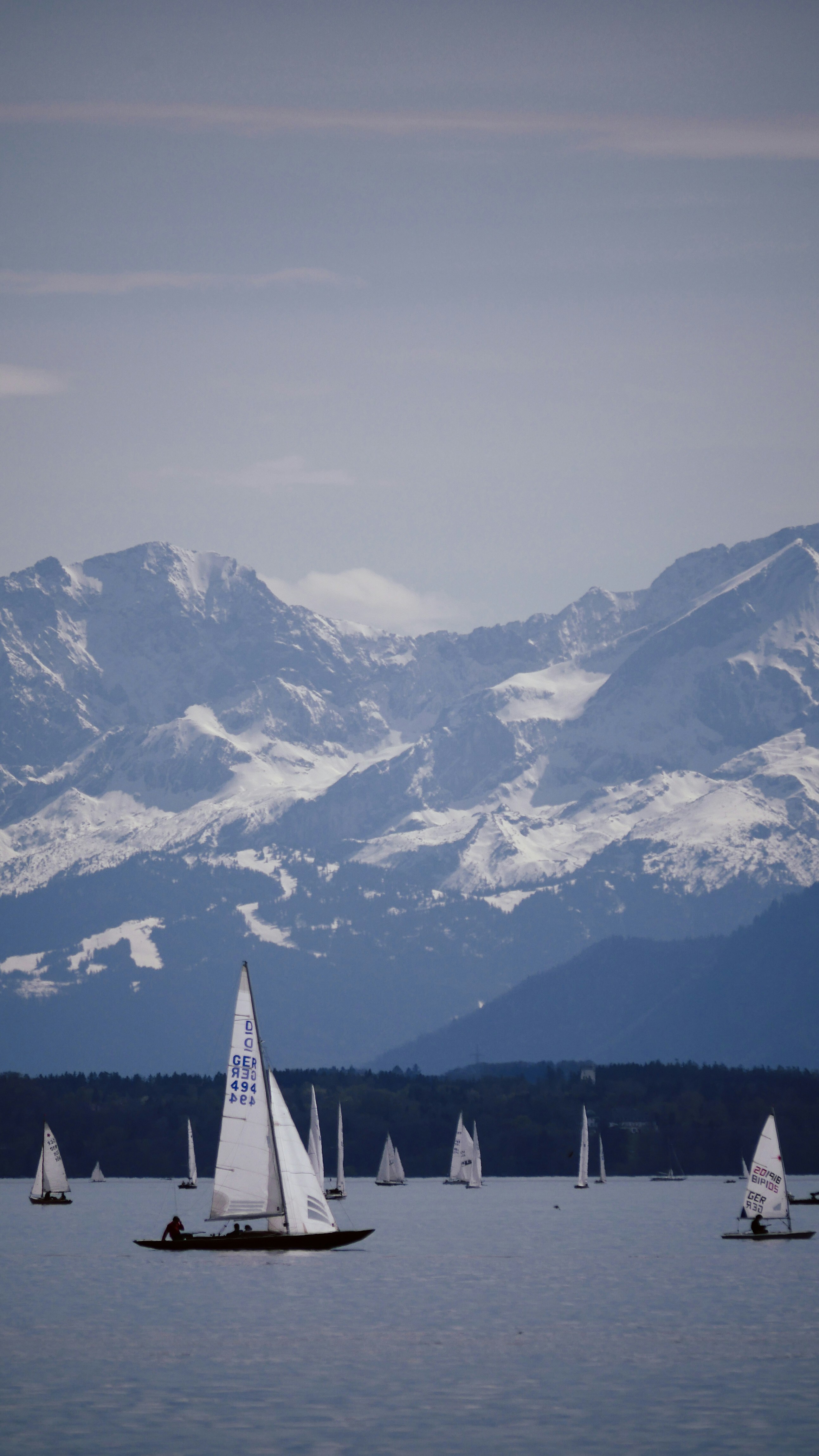 Alpine Sailfleet: A Foreground Sailboat on a Tranquil Lake Beneath Snowbound Peaks