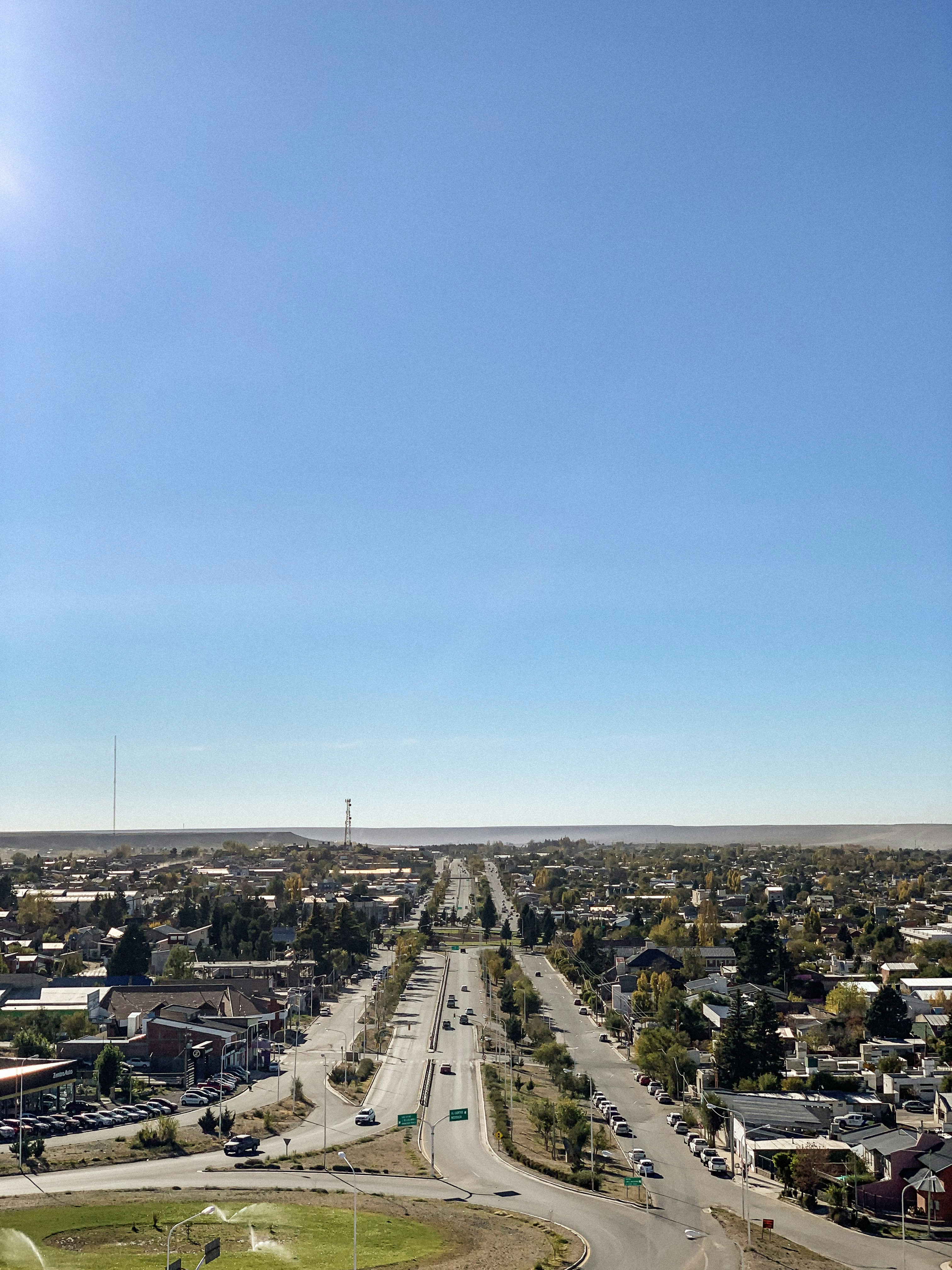 Aerial view of a bustling town with roads and buildings stretching towards the horizon under a bright blue sky.
