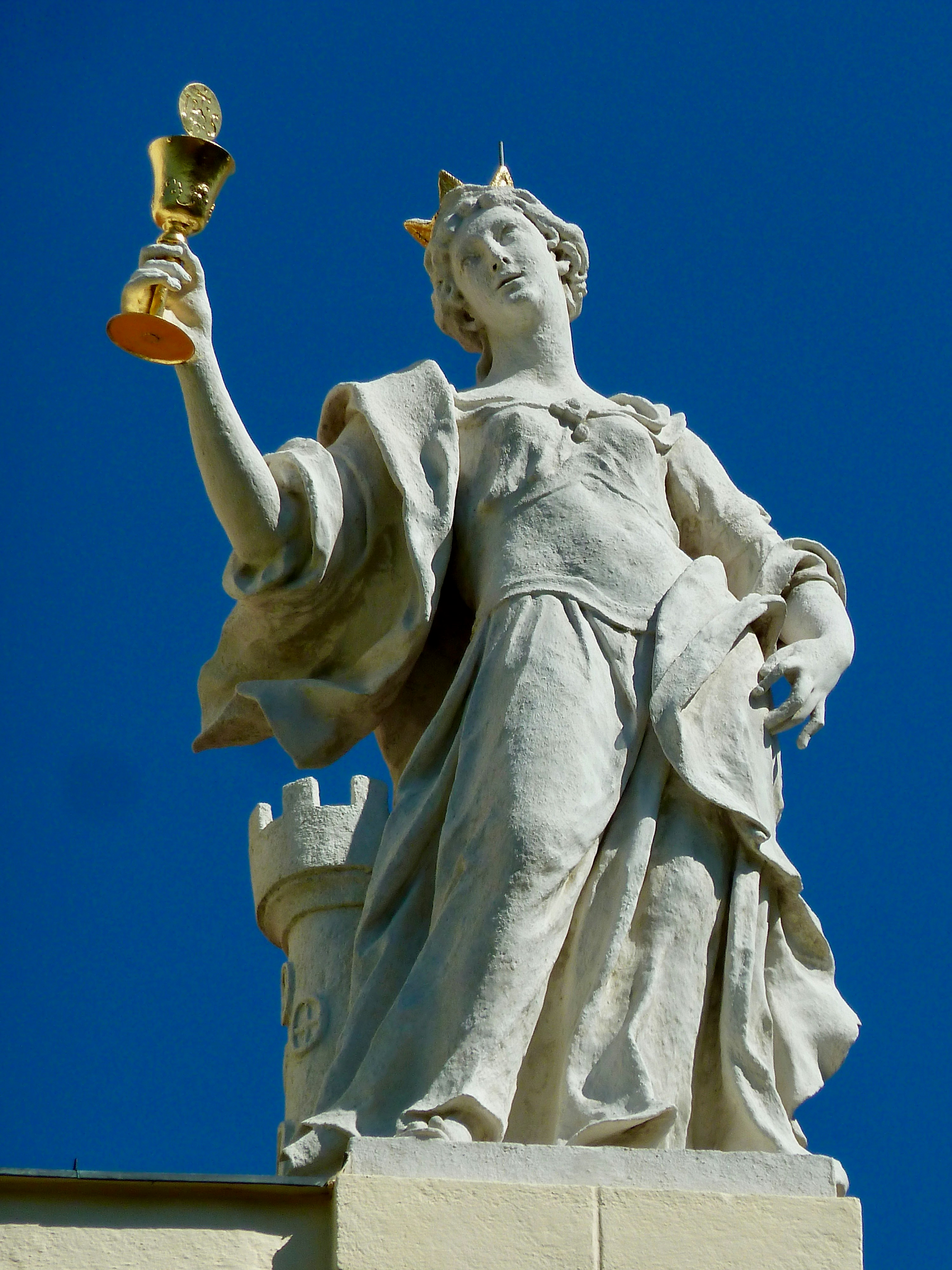 A majestic statue holding a golden chalice, symbolizing victory, against a clear blue sky.