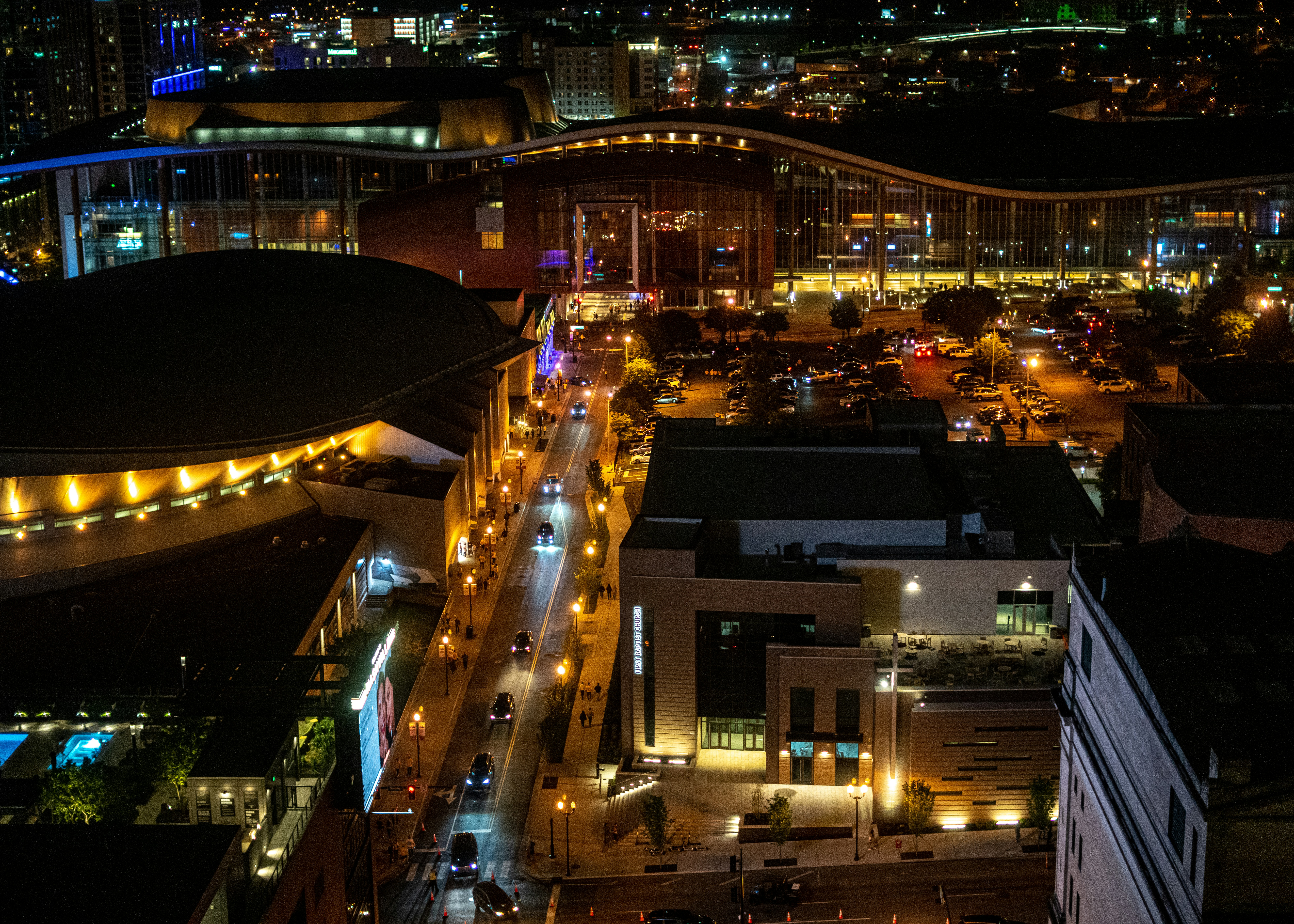 Aerial view of a bustling city at night, showcasing illuminated buildings and busy streets filled with cars. The scene captures the vibrant energy of urban life after dark.