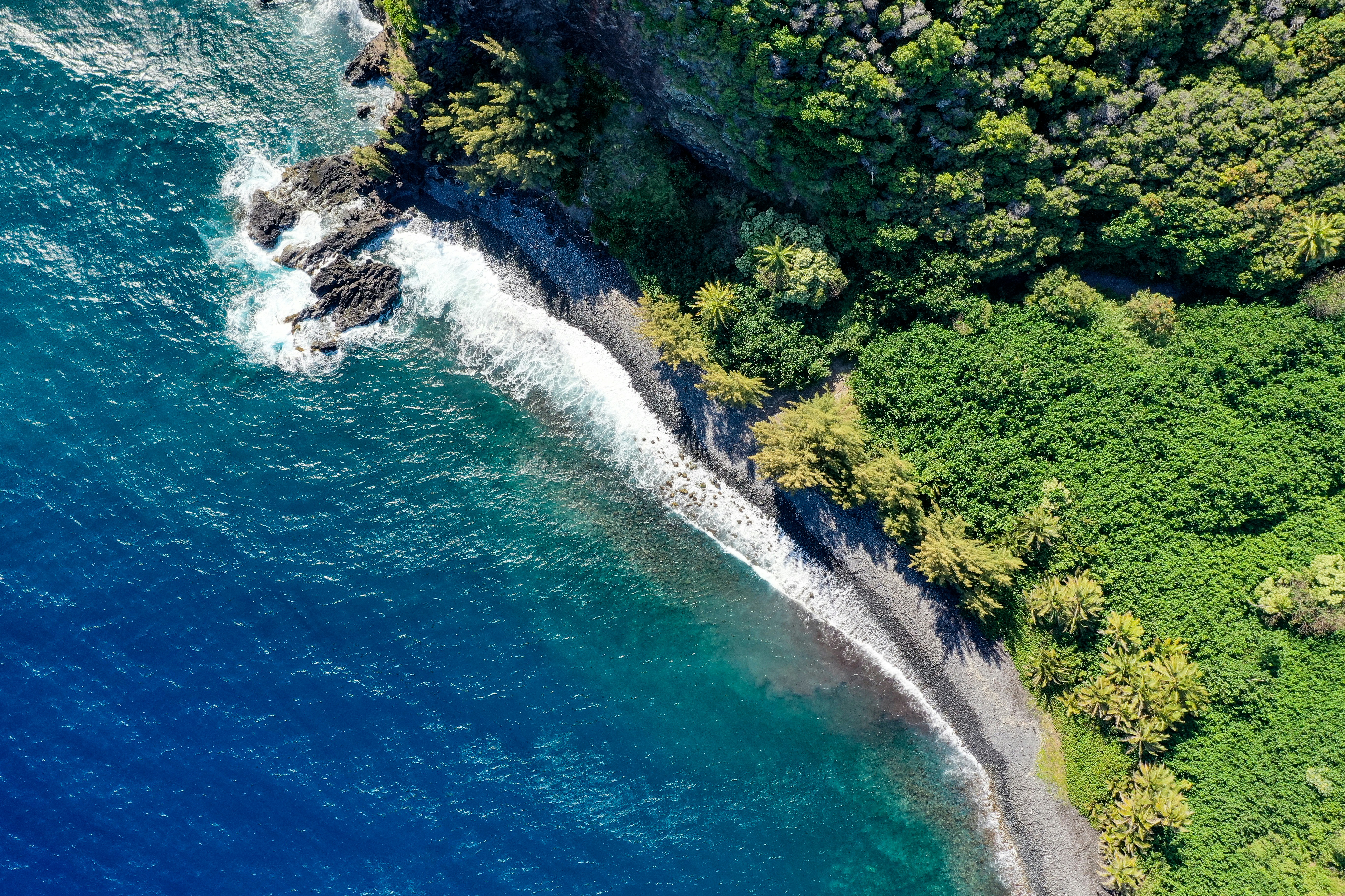 Aerial view of a secluded coastline featuring rocky outcrops, lush greenery, and gentle waves lapping at the shore.