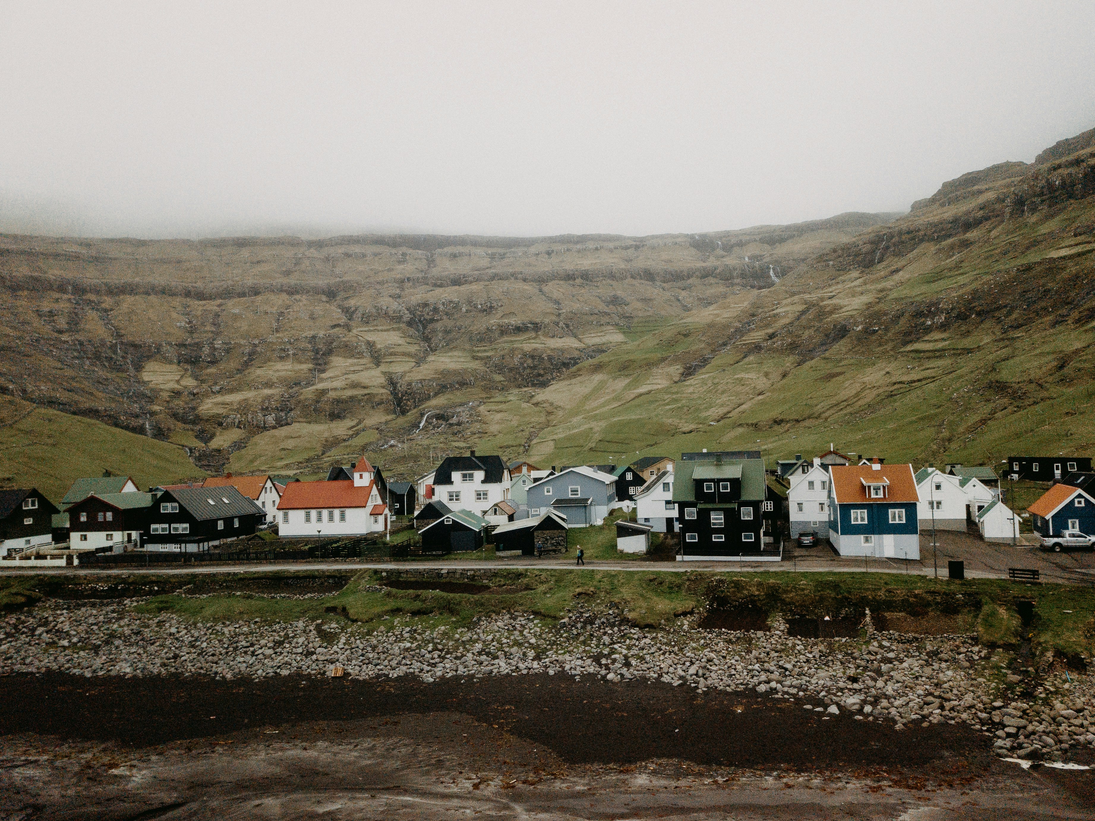 A quaint coastal village with colorful houses set against a backdrop of rugged cliffs and a foggy sky. The scene captures the serene beauty of remote living.