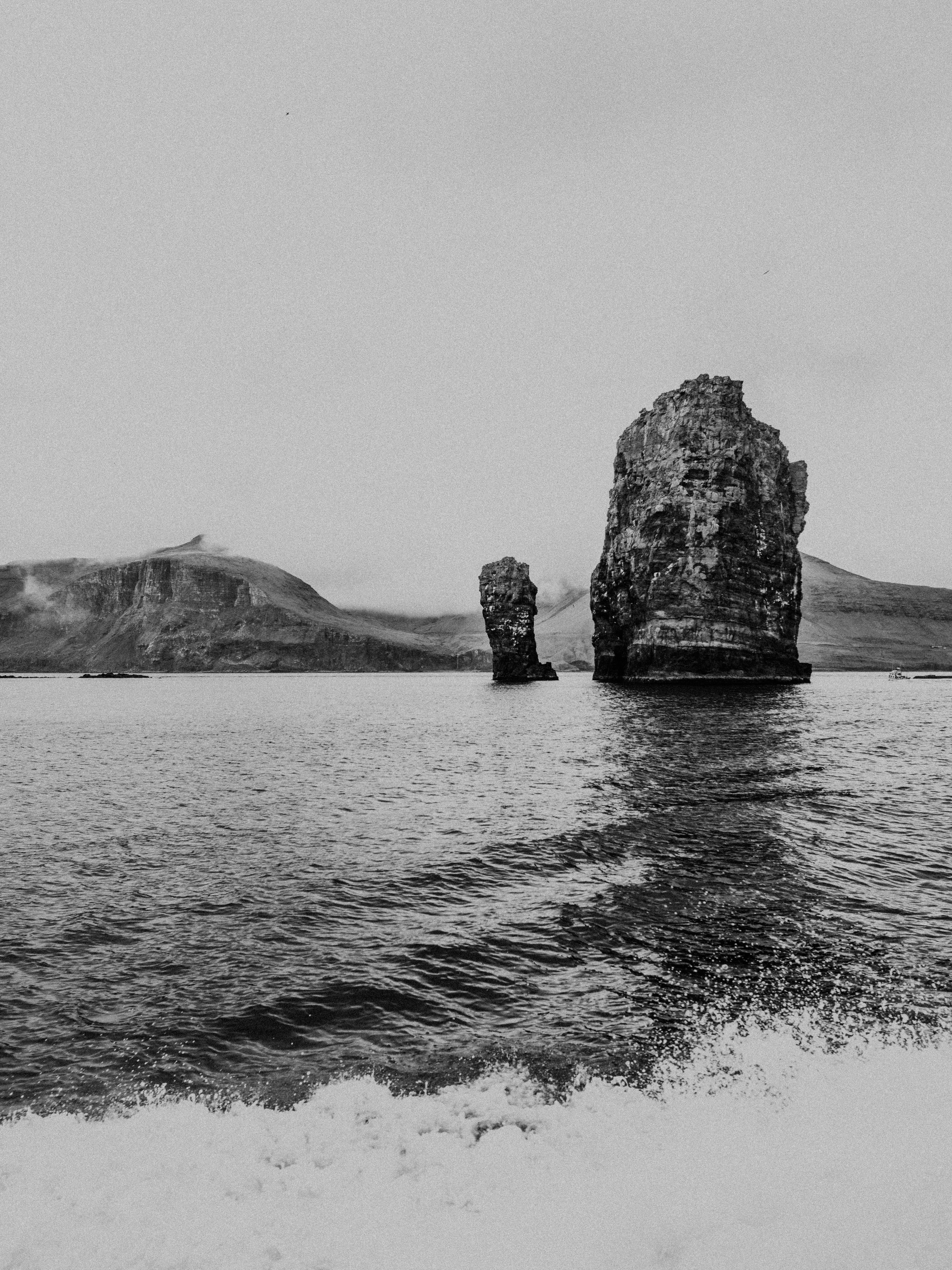 Two towering rock formations rise from the tranquil waters, surrounded by a misty landscape. The monochrome tones enhance the dramatic atmosphere.