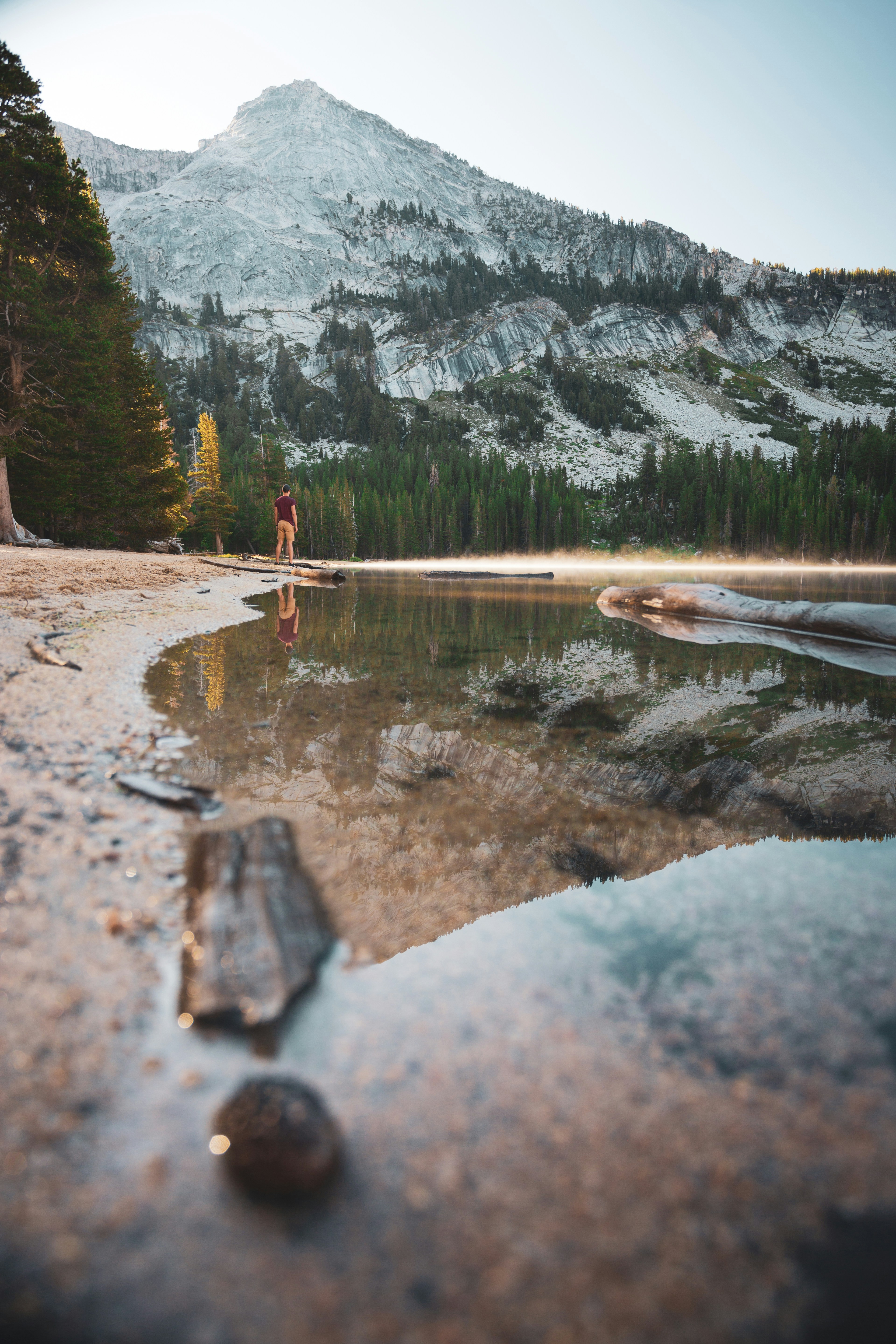 Lone Hiker at the Glassy Alpine Lake Beneath Snowy Peaks