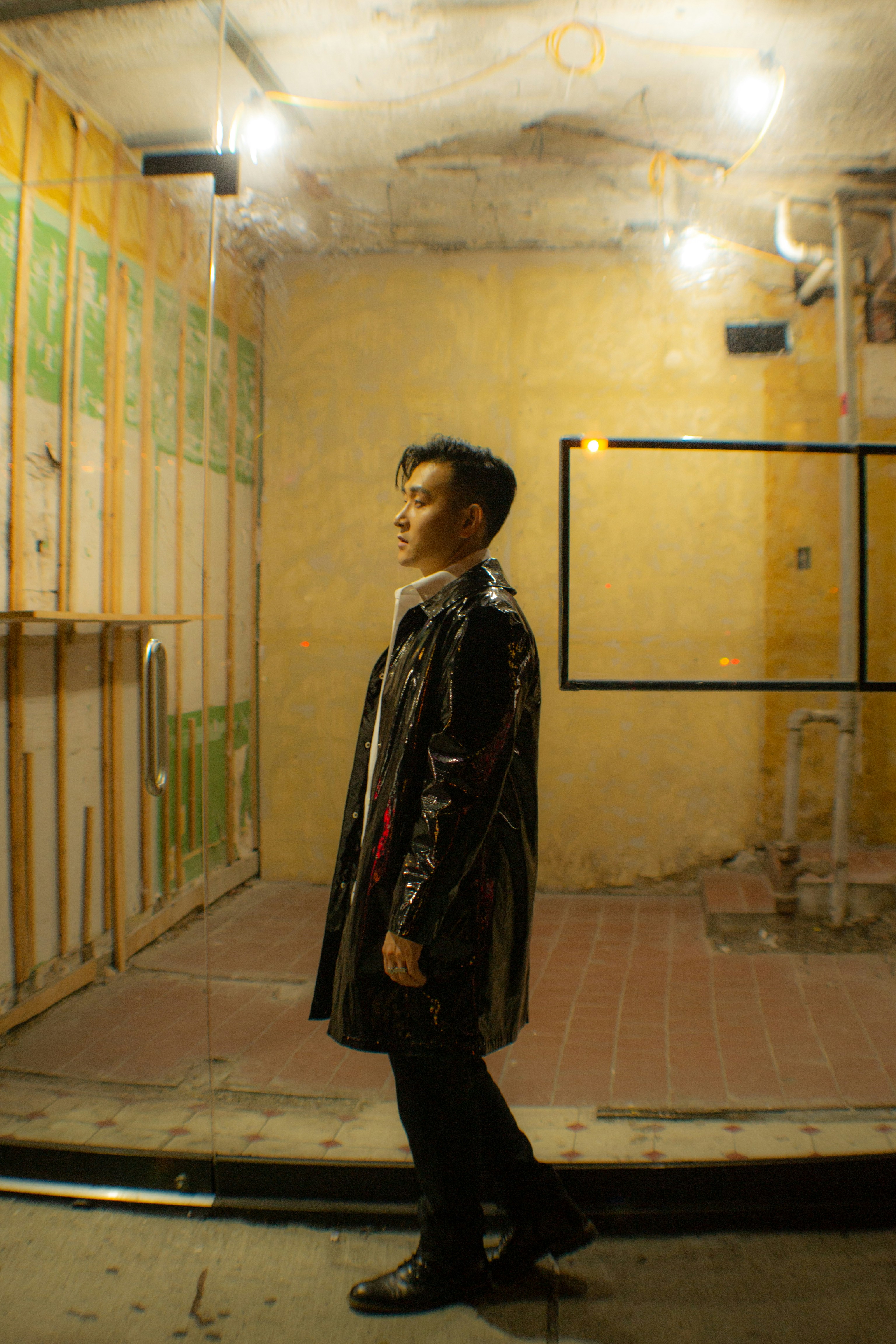 Glossy Trench in a Glass Box: A Quiet Portrait Amid Unfinished Walls