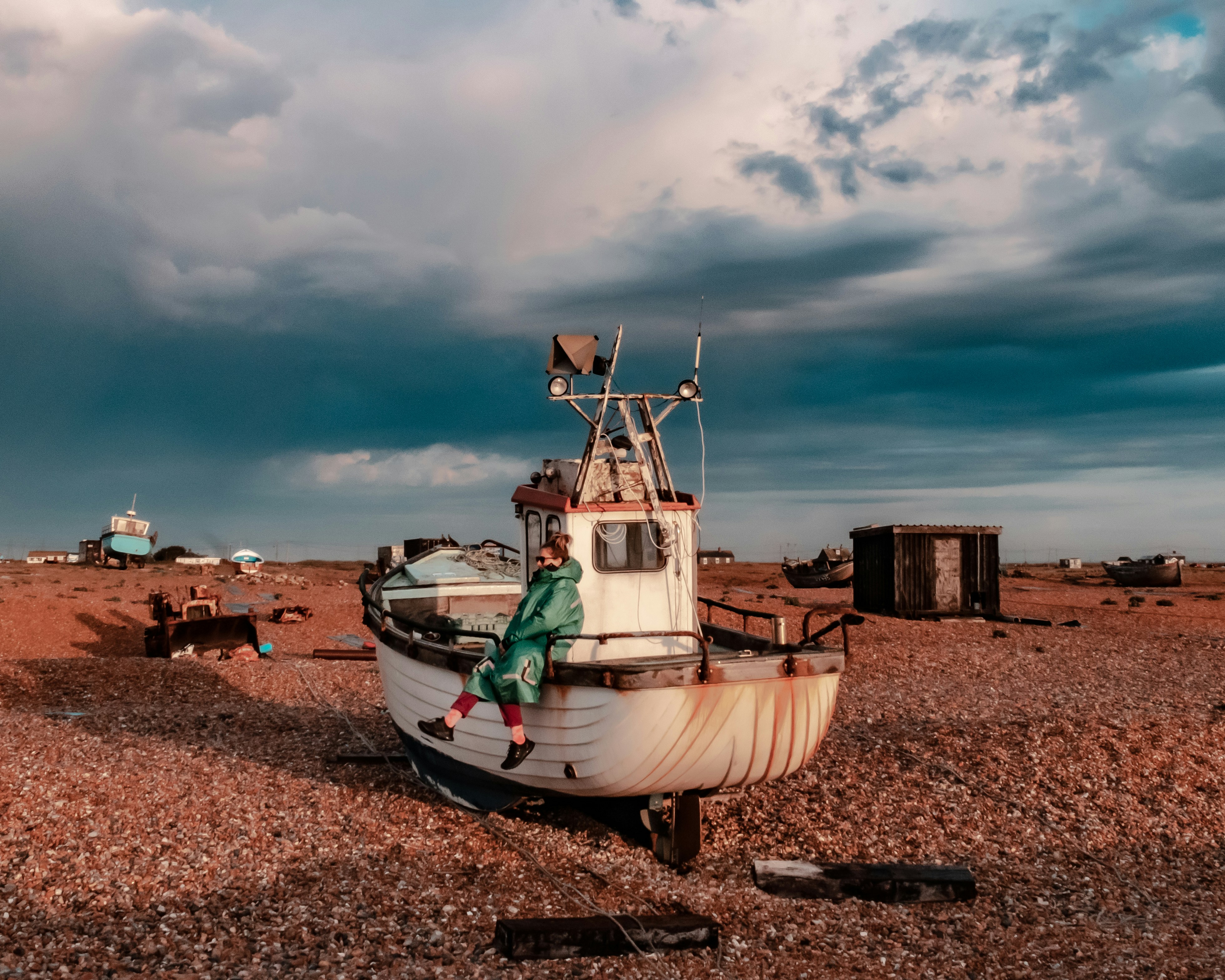 Green-Coated Figure on a Weathered Boat Beneath a Dramatic Coastal Sky