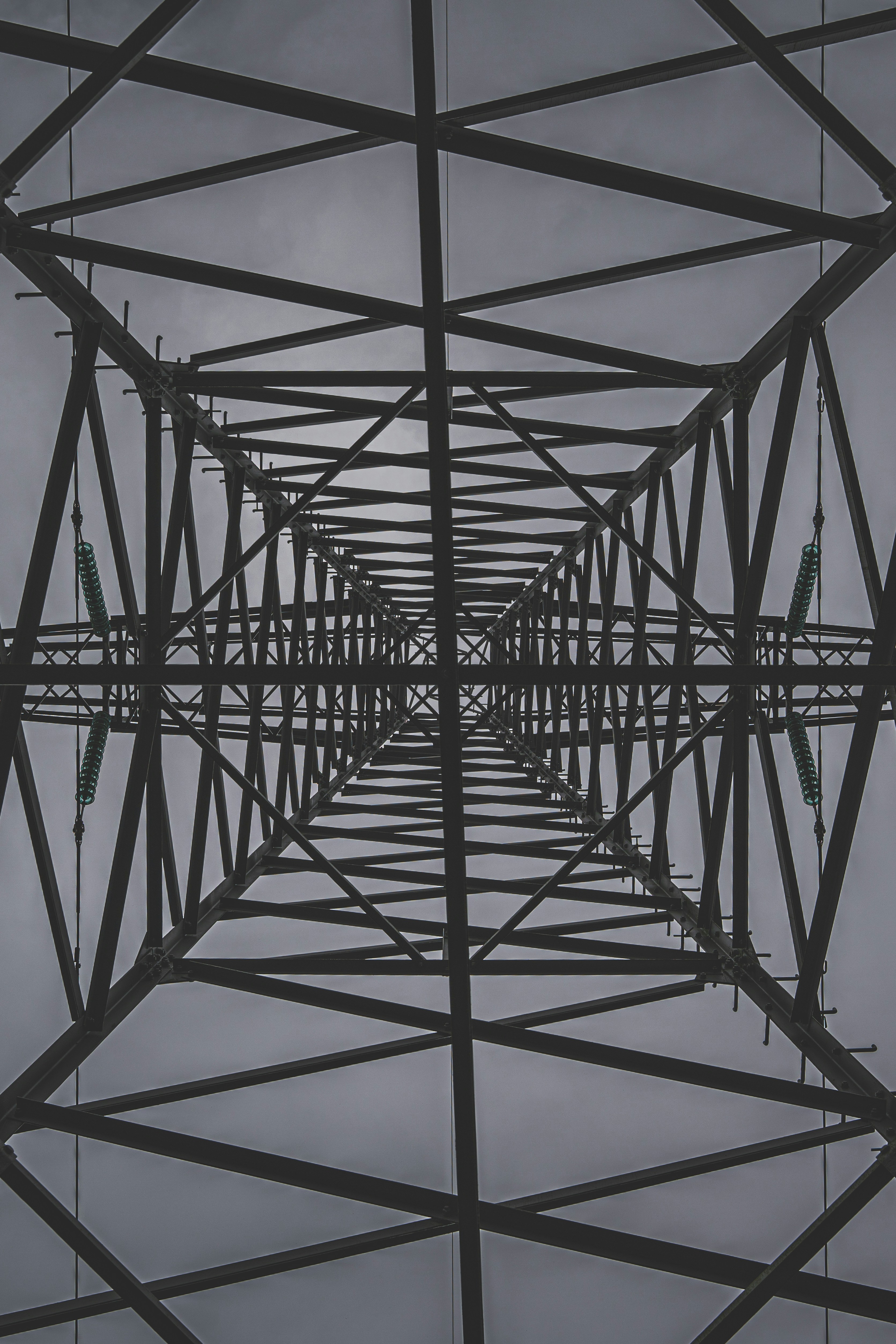 Intricate steel framework of a transmission tower viewed from below, showcasing the symmetry and engineering design. Dark clouds loom overhead.