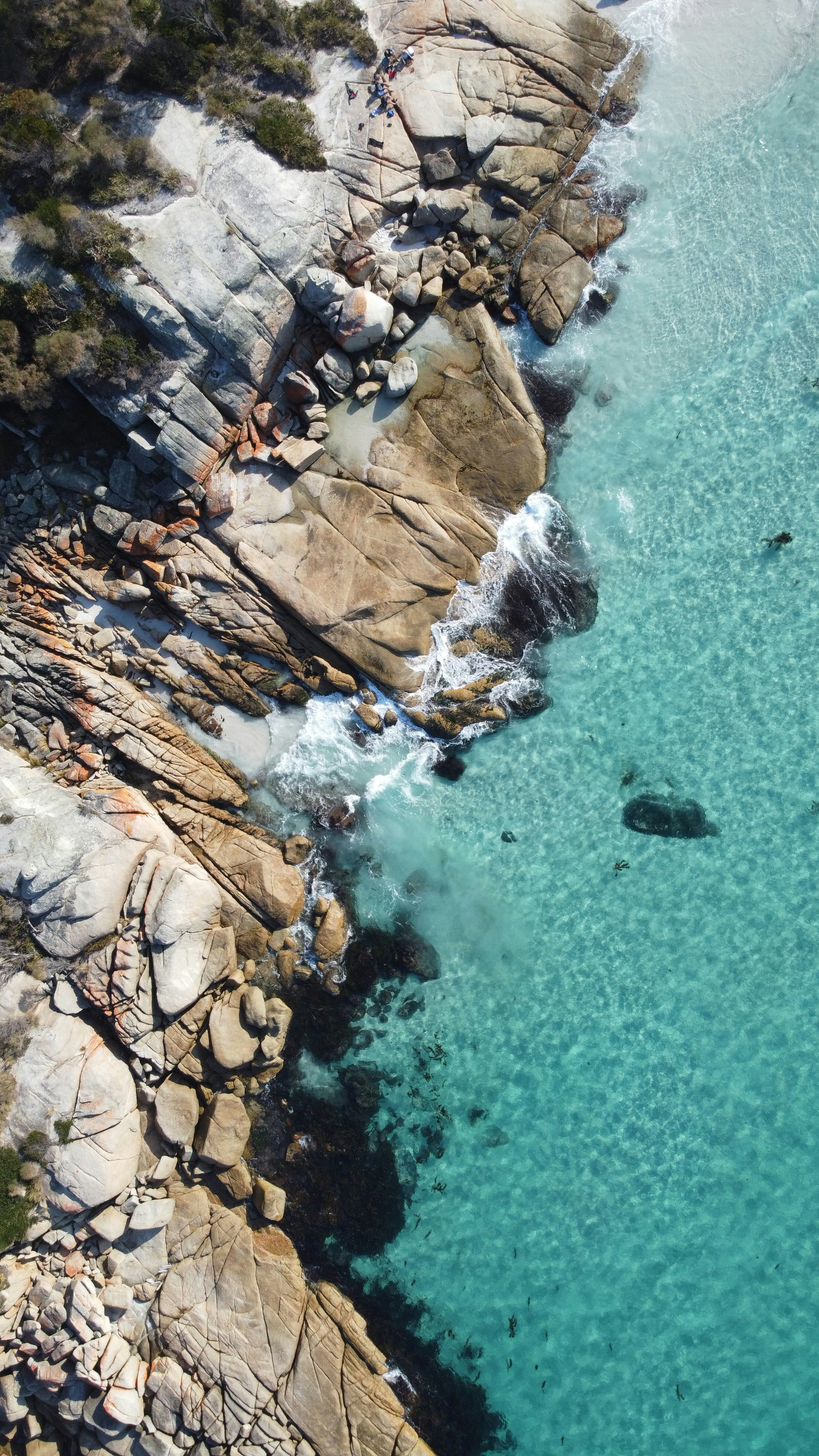 Aerial view of rugged coastline with smooth rocks and turquoise waters, showcasing the interplay between land and sea. Waves gently lap against the shore.
